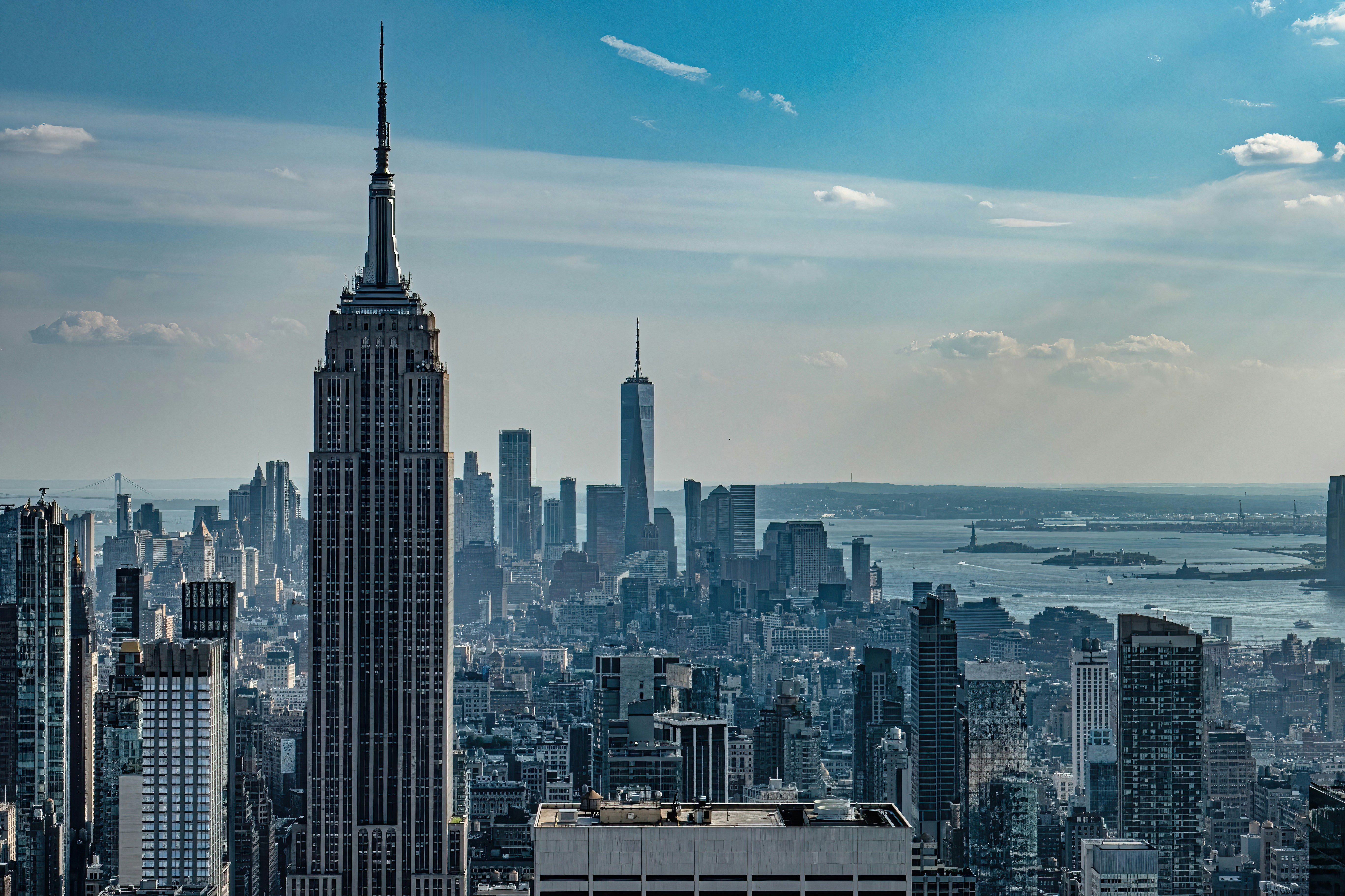 The Empire State Building towers majestically over New York City, framed by a sprawling urban landscape and a serene harbor in the distance.