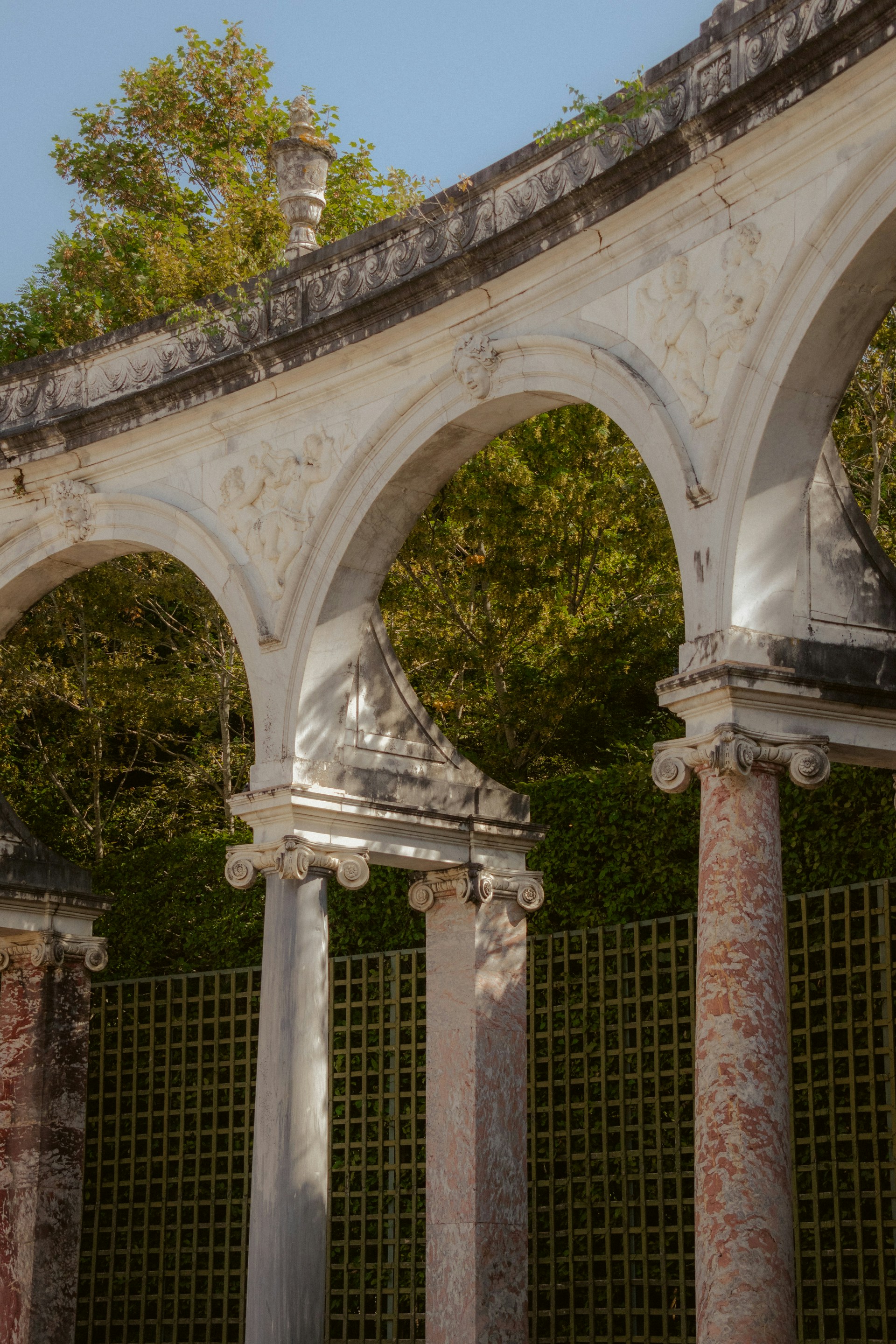 Intricate architectural arches adorned with classical motifs, framed by lush greenery and a trellis backdrop.