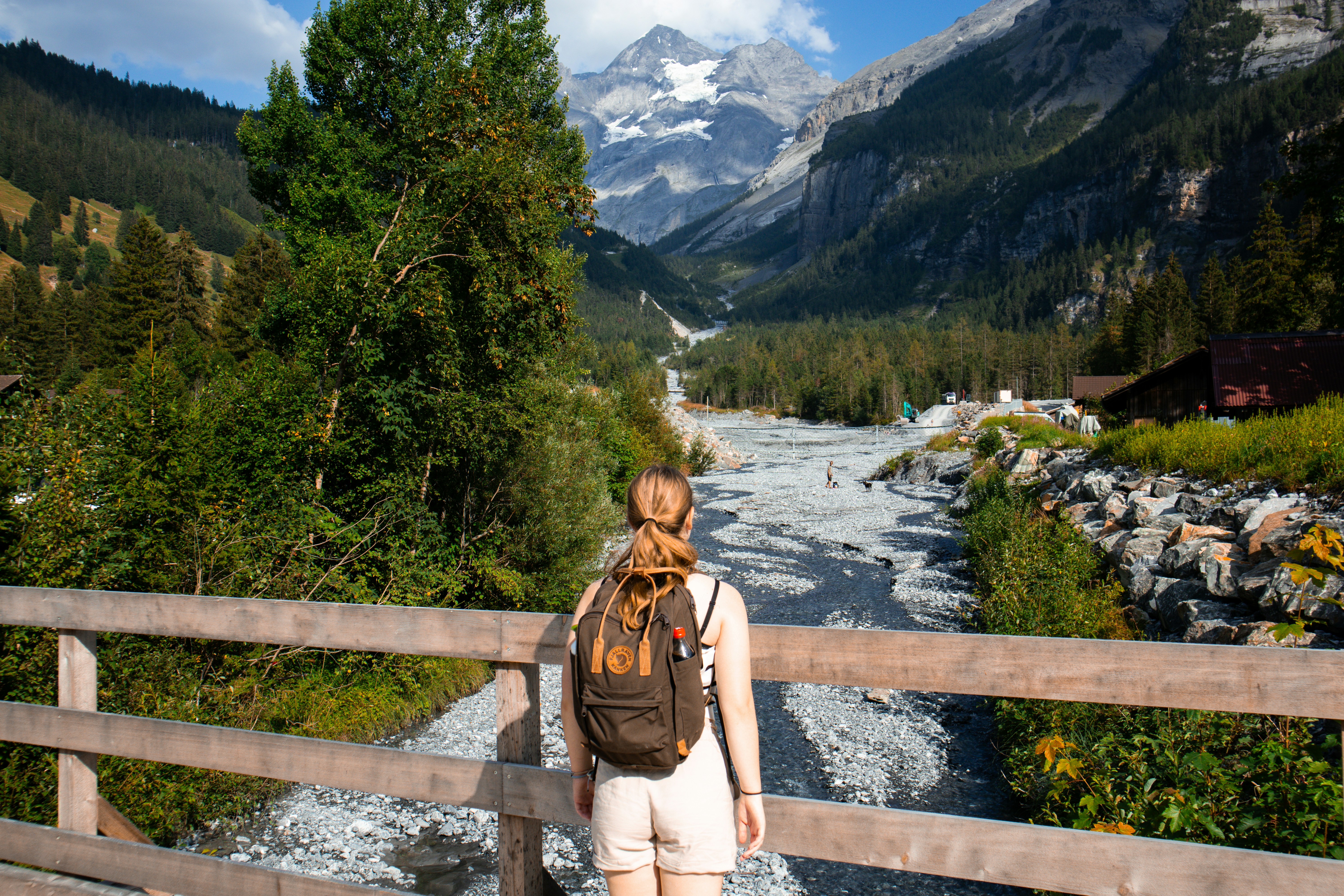 Hiker on a wooden bridge toward alpine river and mountains