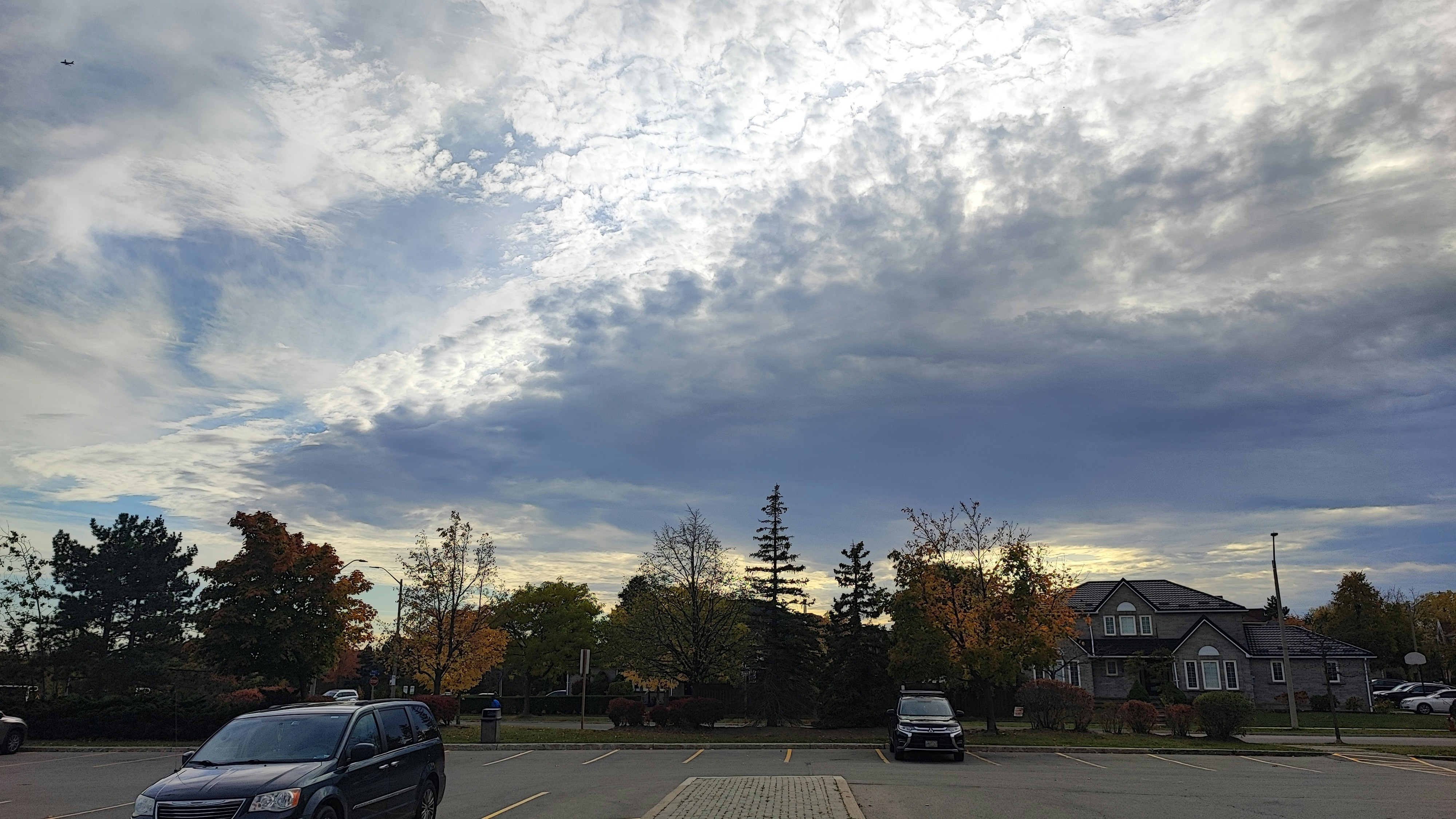 Suburban cul-de-sac at dusk with parked cars, autumn trees, and a dramatic cloud-filled sky.