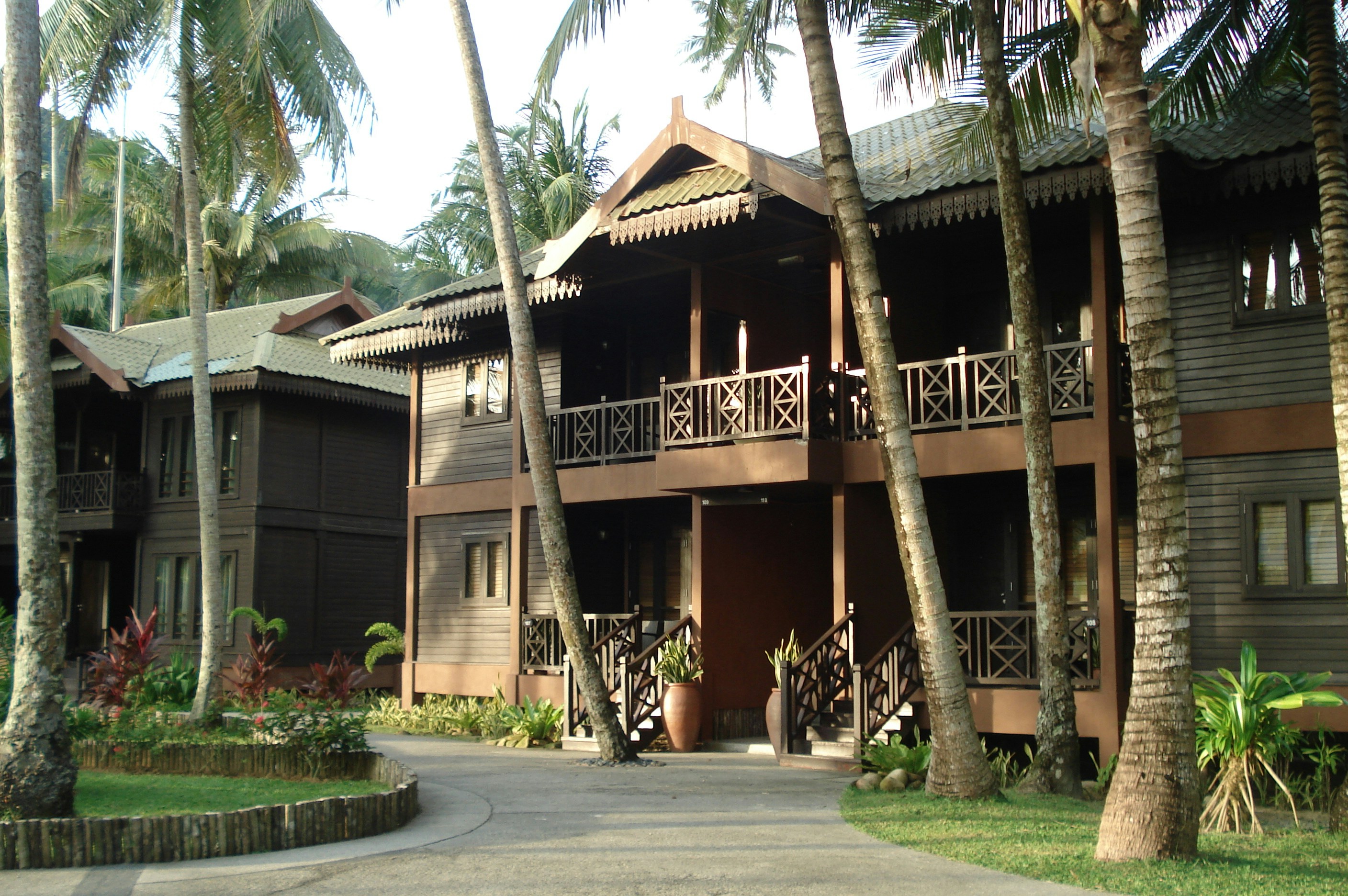 Wooden resort building surrounded by lush palm trees and vibrant tropical plants, inviting relaxation and tranquility.
