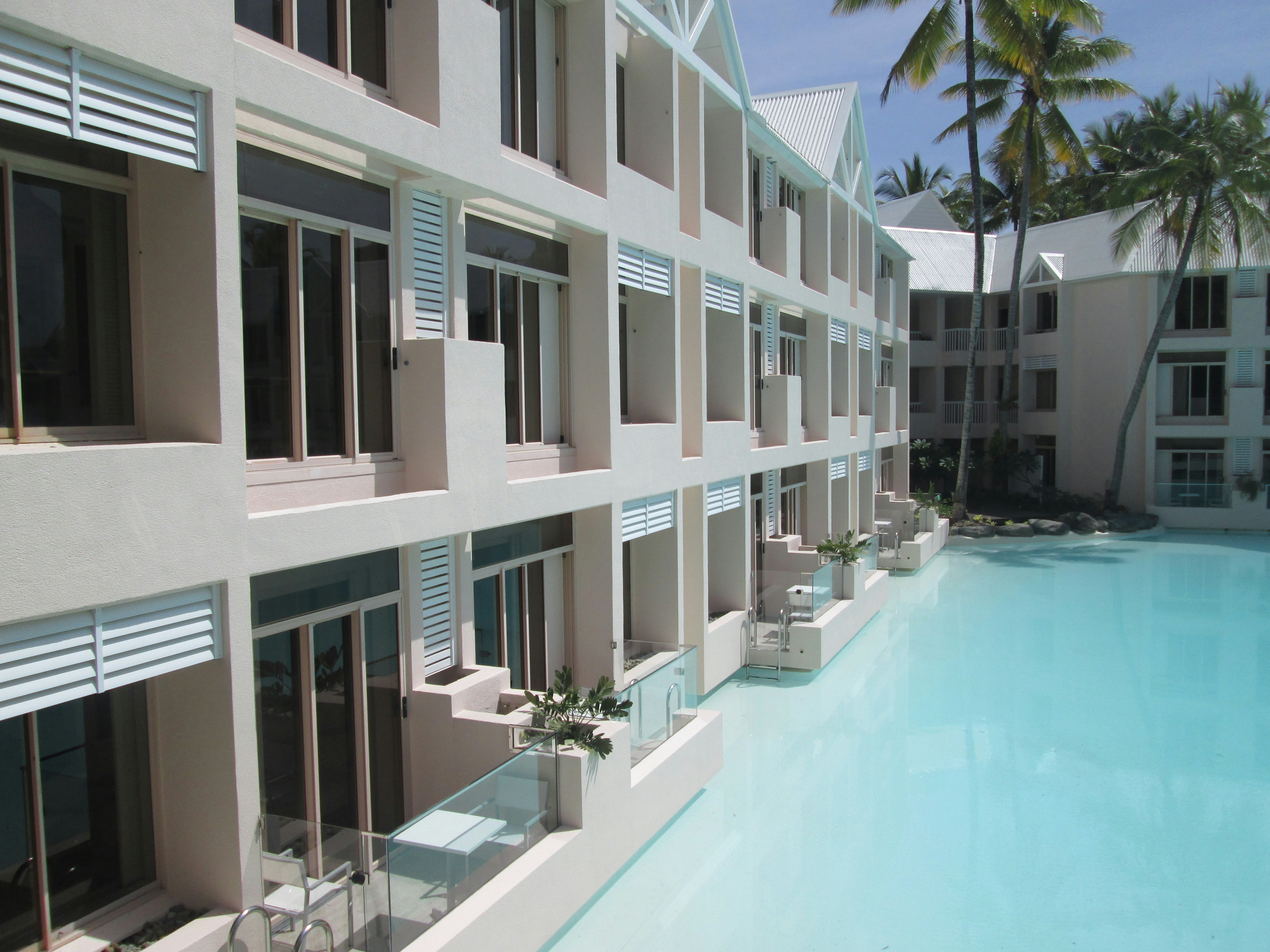Modern resort buildings with balconies overlooking a tranquil turquoise pool under a clear blue sky.