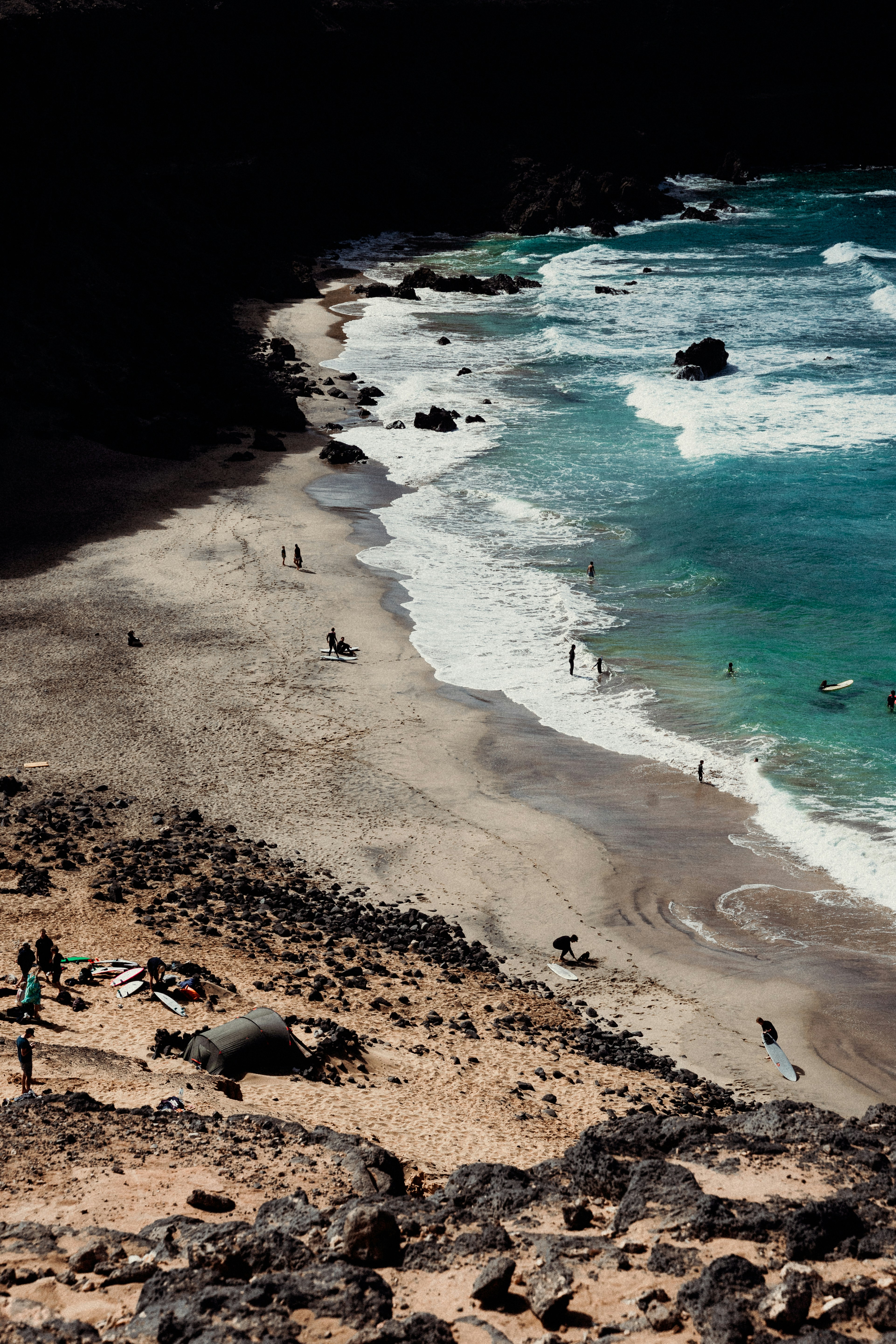 A serene beach scene with surfers and beachgoers enjoying the turquoise waters and rocky coastline. The contrast of sand and waves creates a tranquil atmosphere.