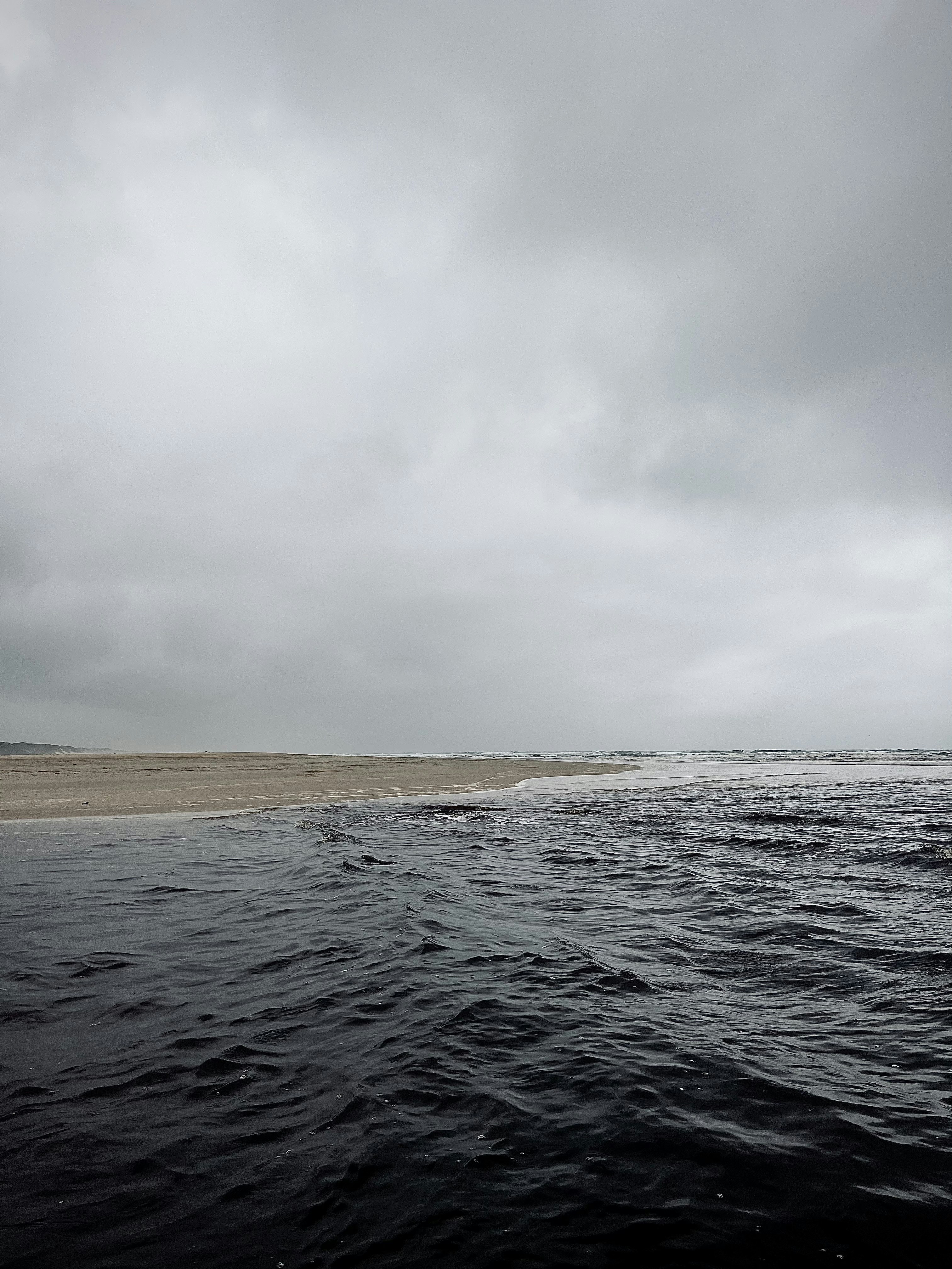 Dark waters meeting a sandy shoreline beneath a cloud-laden sky.