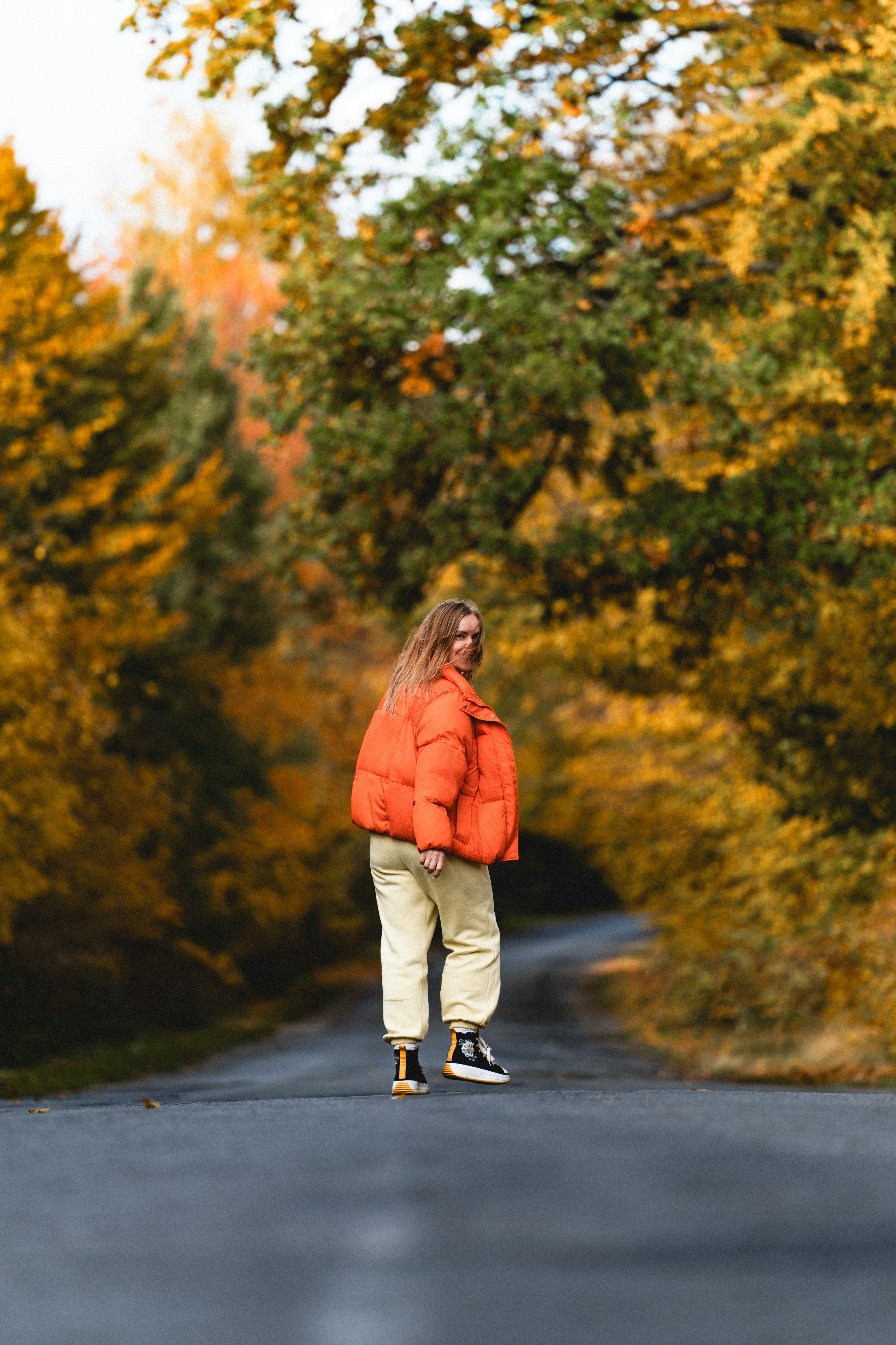 Autumn Quiet: A solitary figure in an orange puffer on a leaf-strewn road