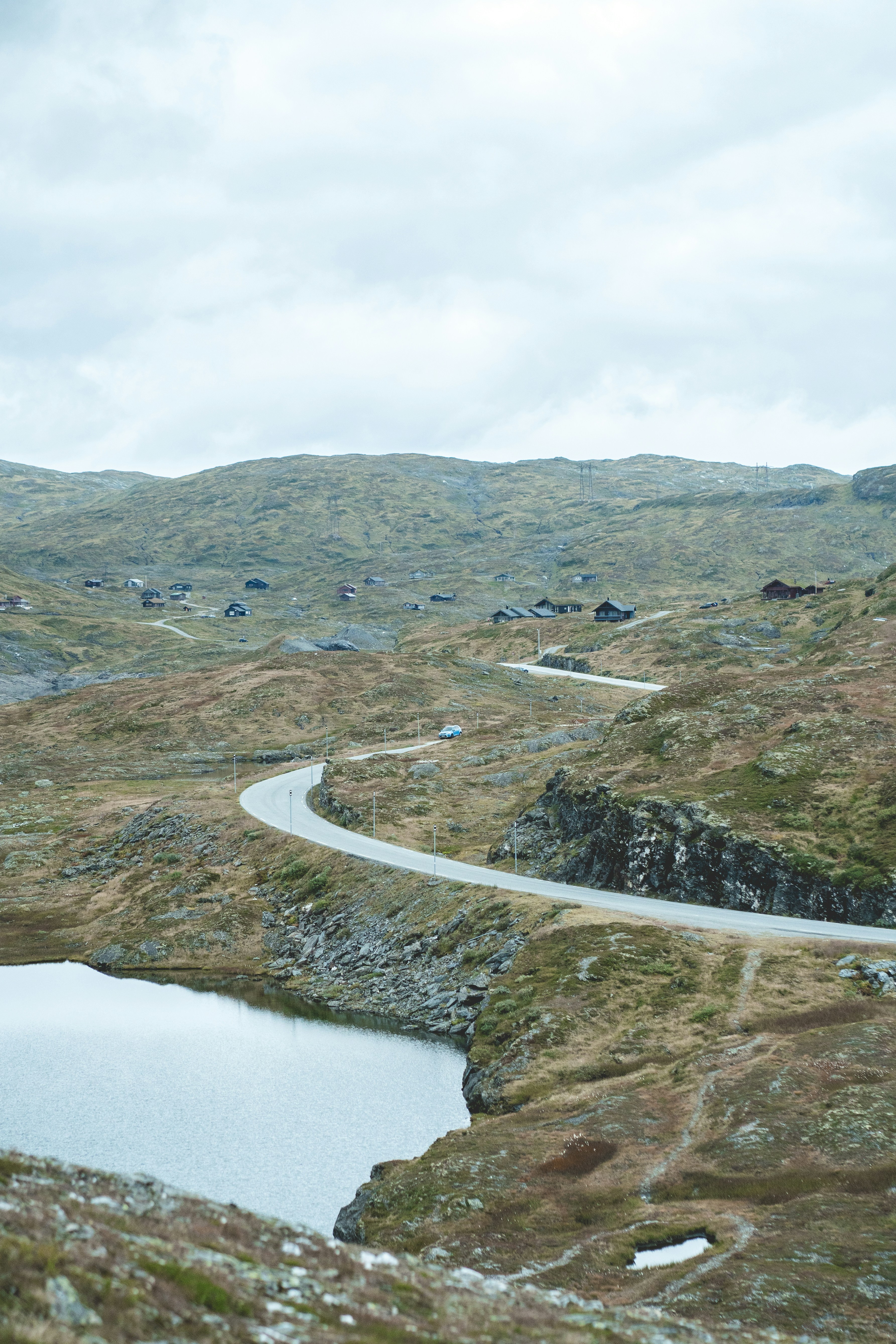 Winding road cutting through rocky hills with a serene lake nestled beside it.