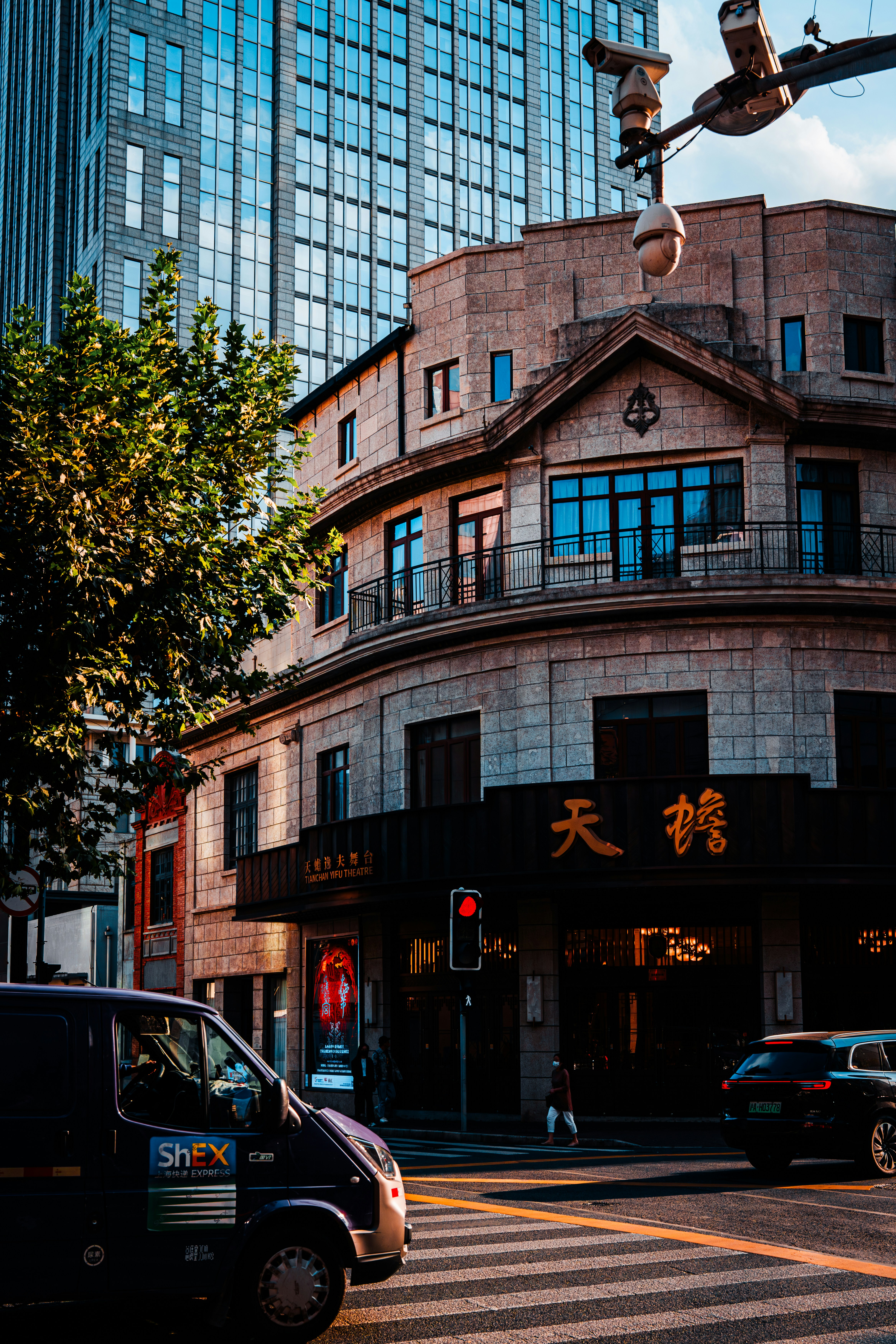 Historic building with modern glass skyscrapers in the background, showcasing a blend of traditional and contemporary architecture. Traffic signals and vehicles add to the urban atmosphere.