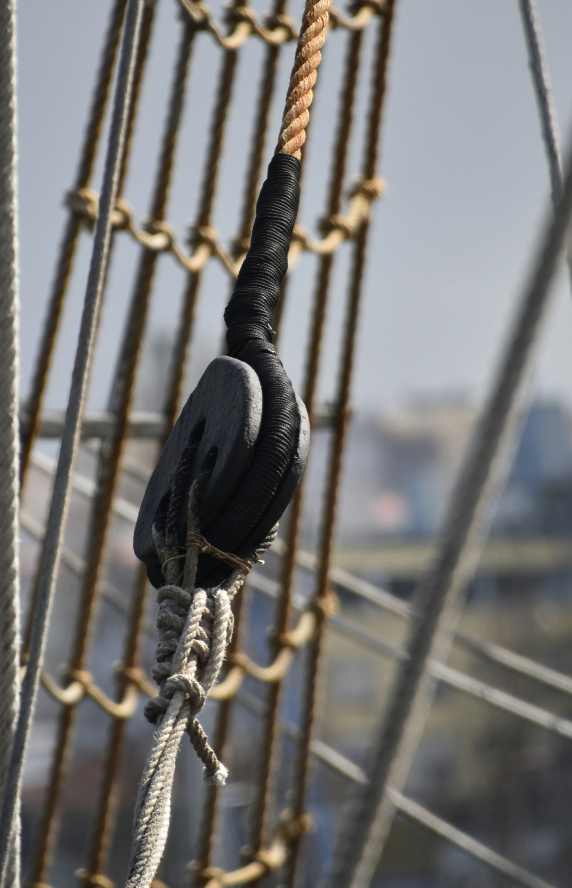 Close-Up on Weathered Rigging: A Pulley Wrapped in Rope Against a Distant Cityscape
