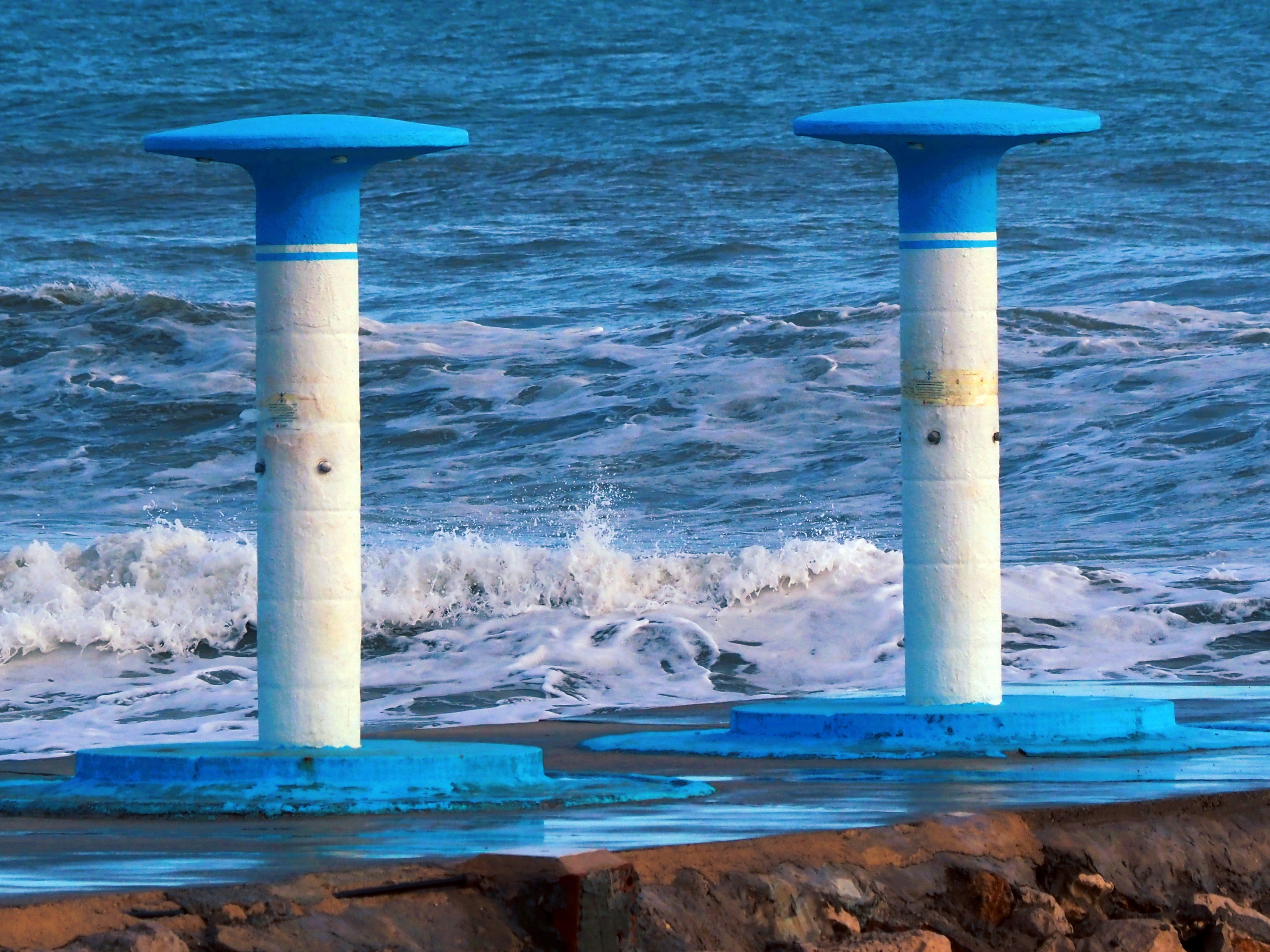 Two blue and white poles sticking out of the ocean photo – Free Mar ...