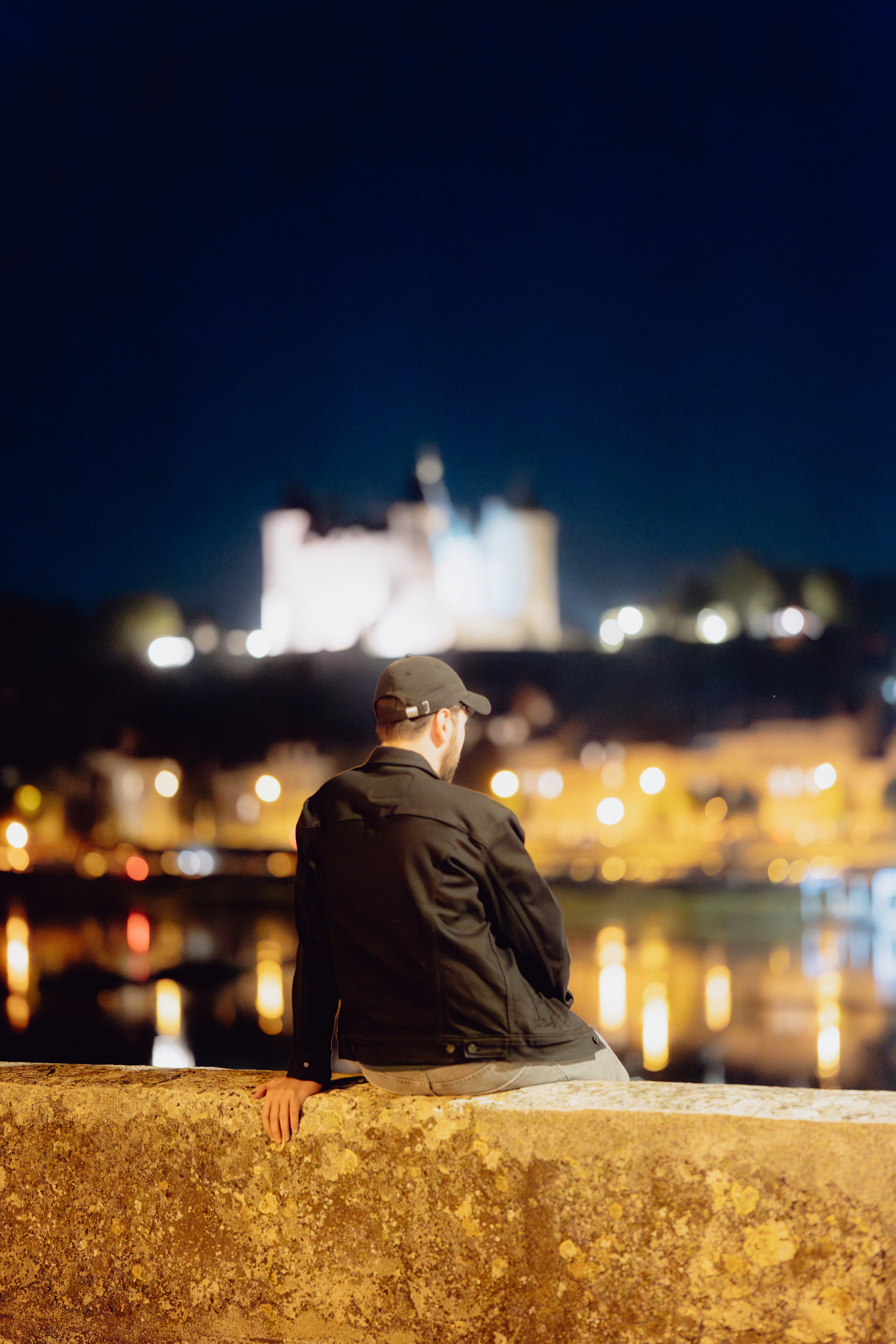 Nightly Riverside Quiet: A Man in a Dark Jacket Gazes Toward the Neon Horizon