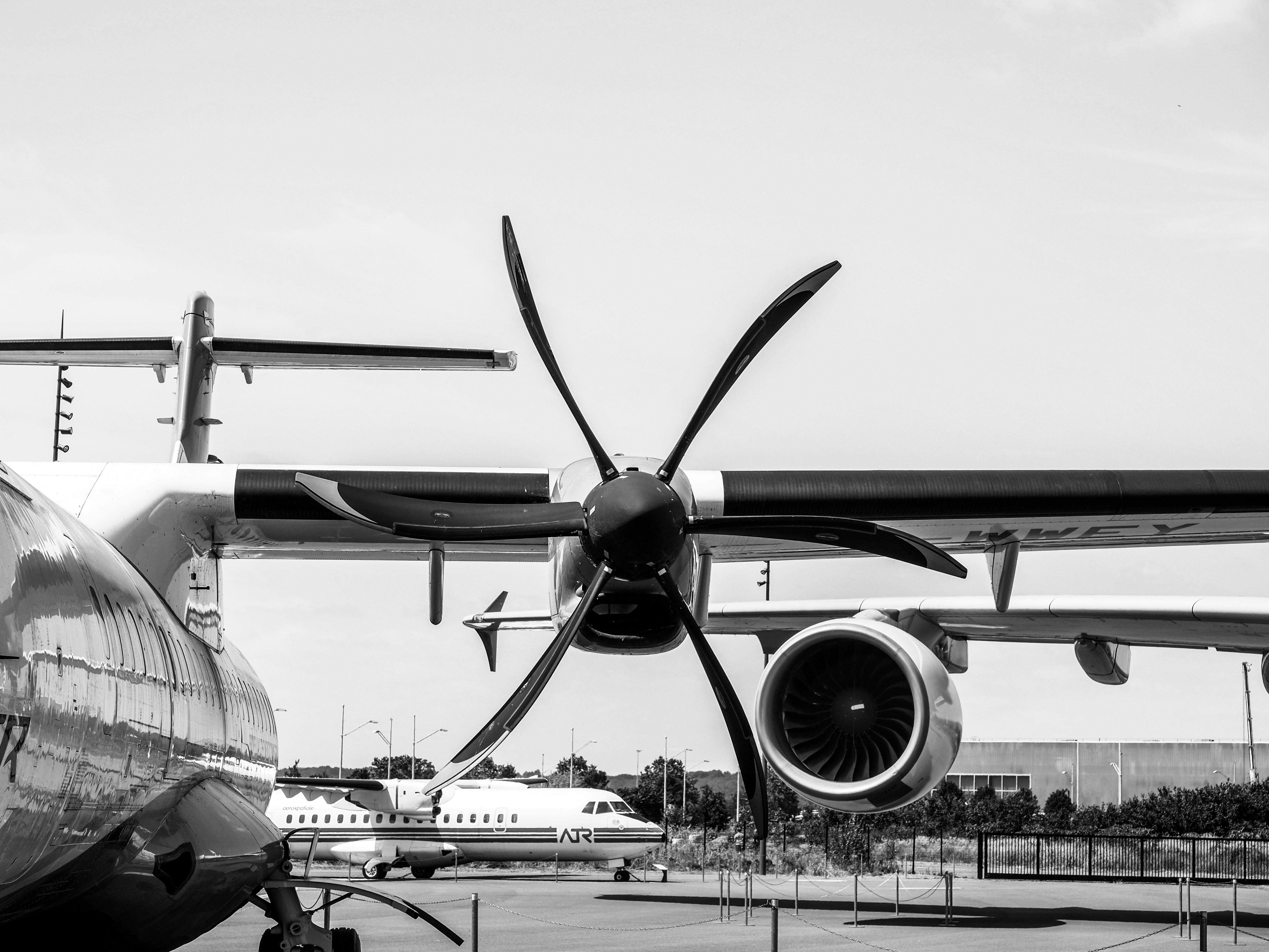 Black-and-white photograph of a propeller-driven aircraft with a jet in the background, highlighting polished metal surfaces and industrial symmetry.