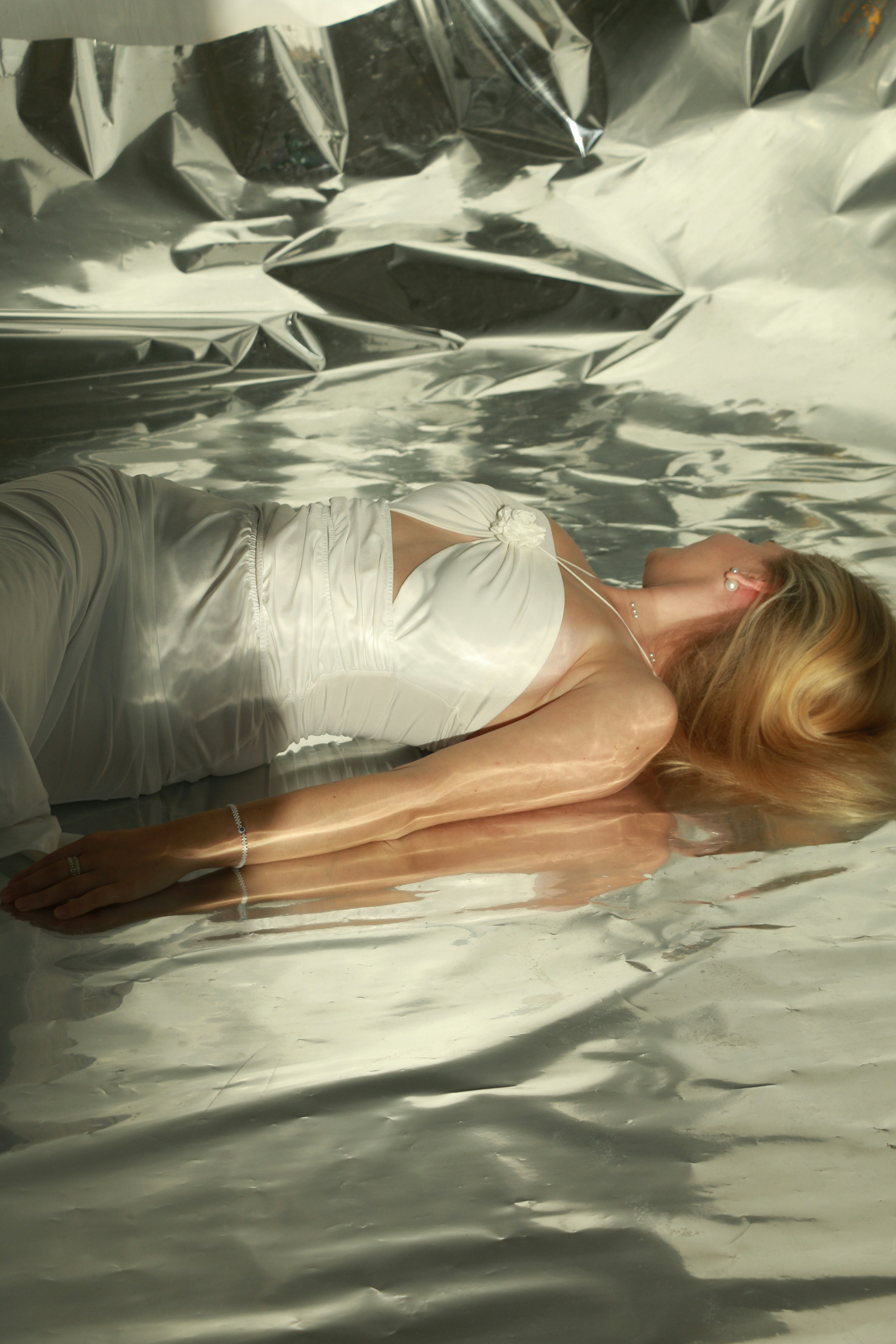A woman in a flowing white gown reclines on a reflective surface, creating a serene interplay of light and shadow.