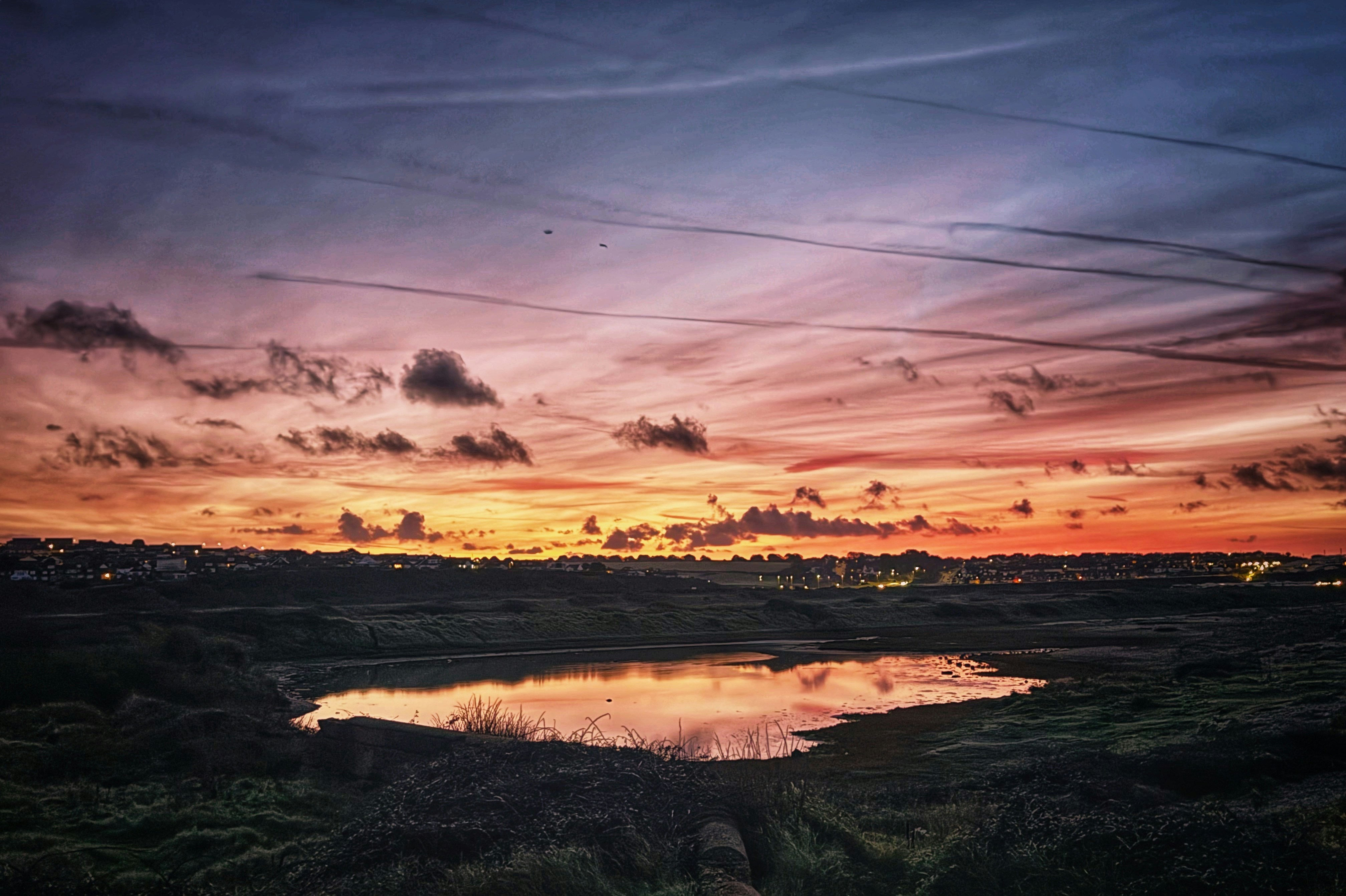 Autumn Sunset showing colorful sky in the Reflection on a small lake. Urban housing in the horizon with feint house lights visible. Photograph taken over Tidemills, Seaford.