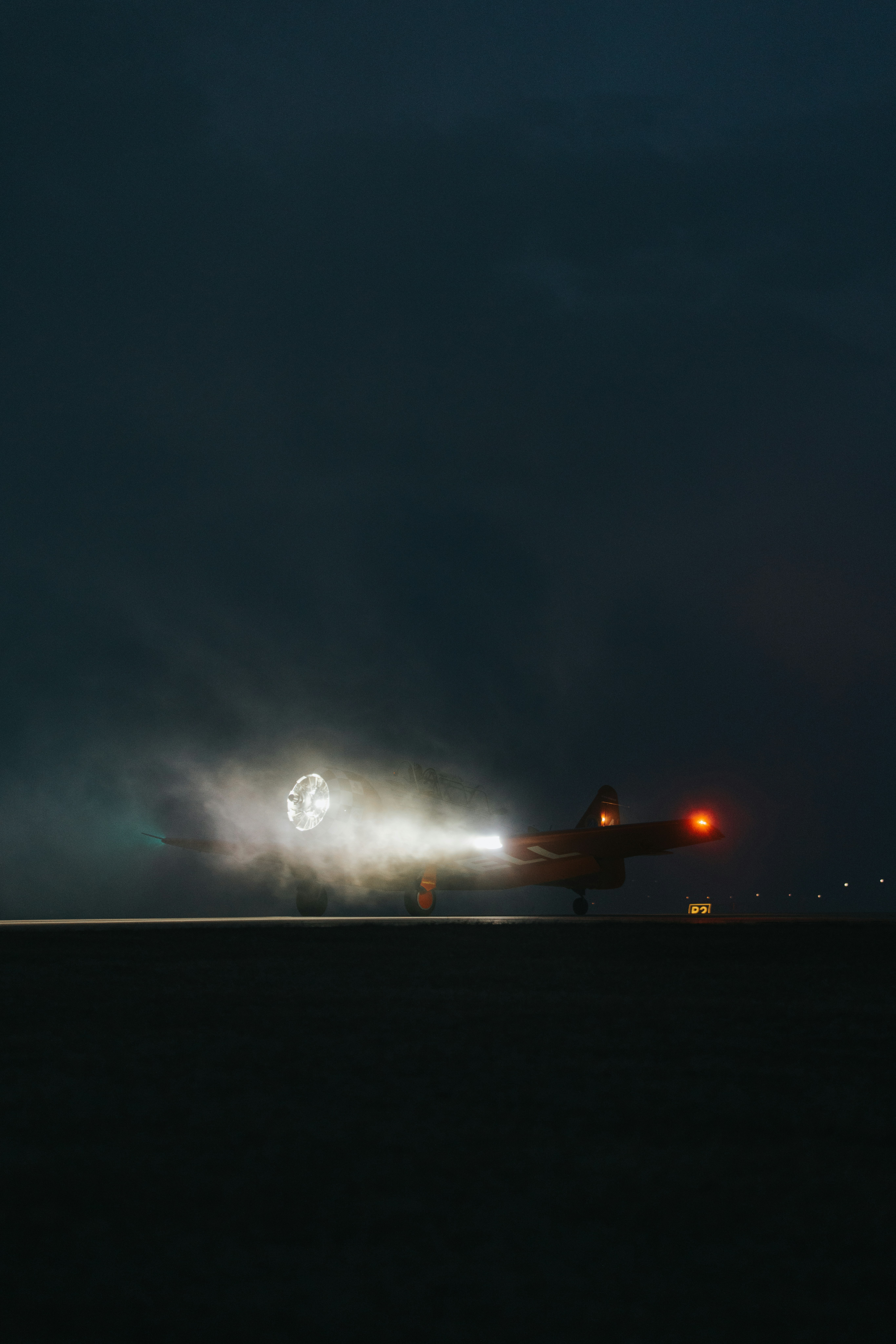 Moonlit Runway: A lone propeller plane carves through mist with red beacon