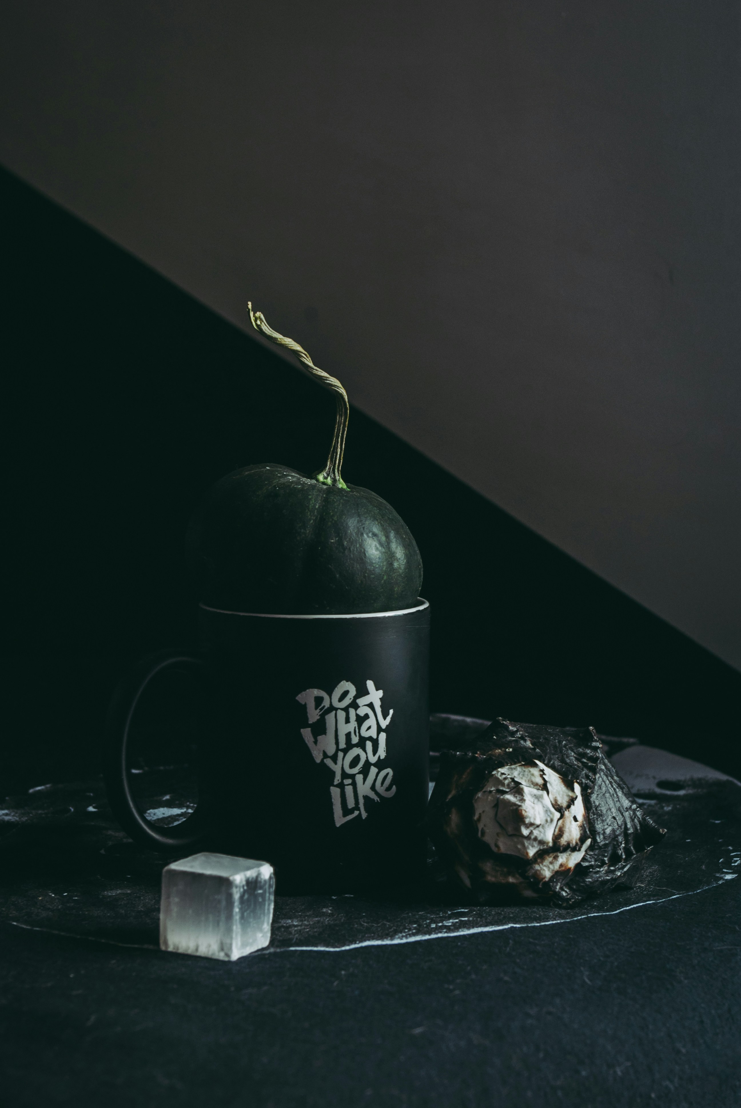 Crowning Quiet: A Pumpkin Reigns Over a Matte Mug in Dim Light