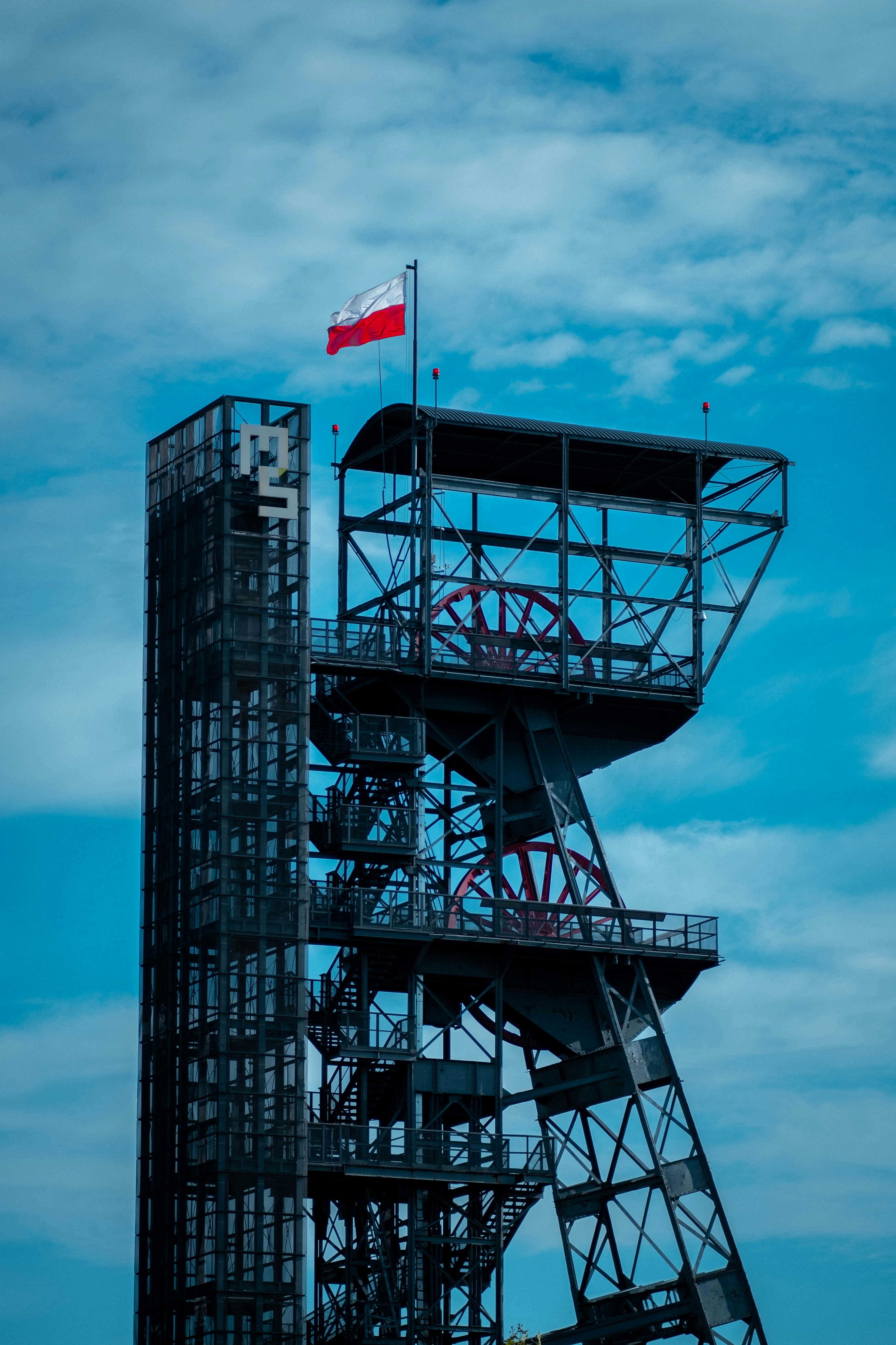 Flag atop an industrial gallery: a steel lattice structure under a bright blue sky