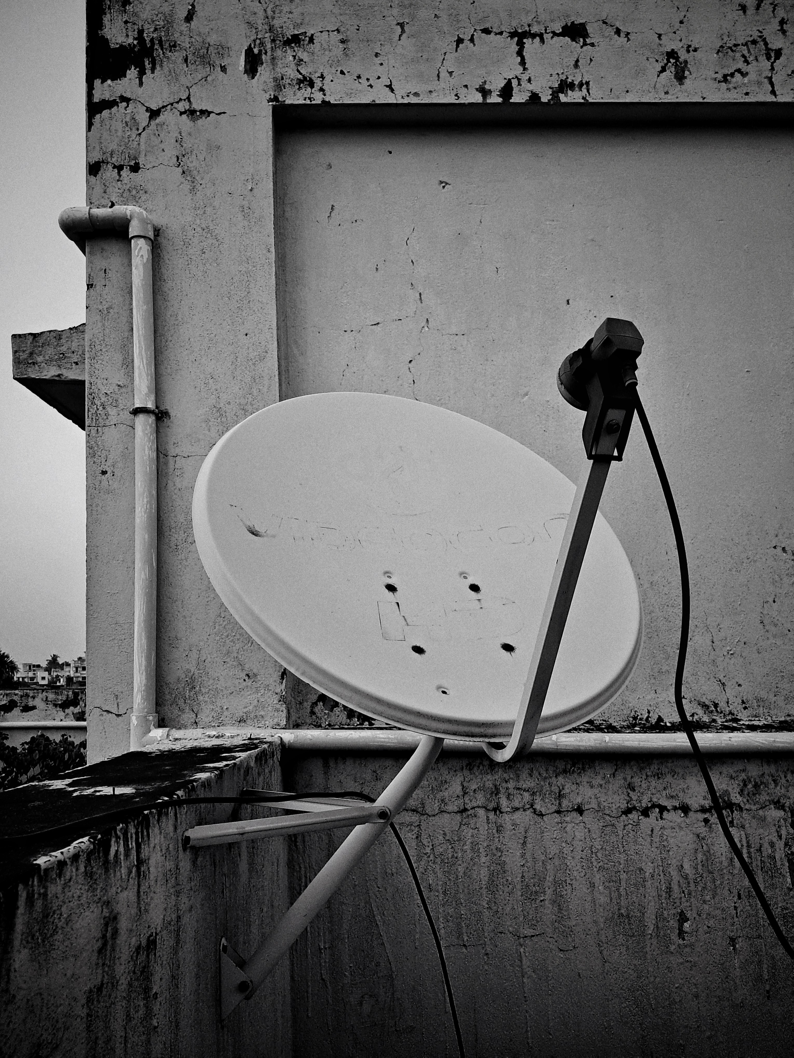 Noir Rooftop Dish: A Satellite's Quiet Angles on a Weathered Wall