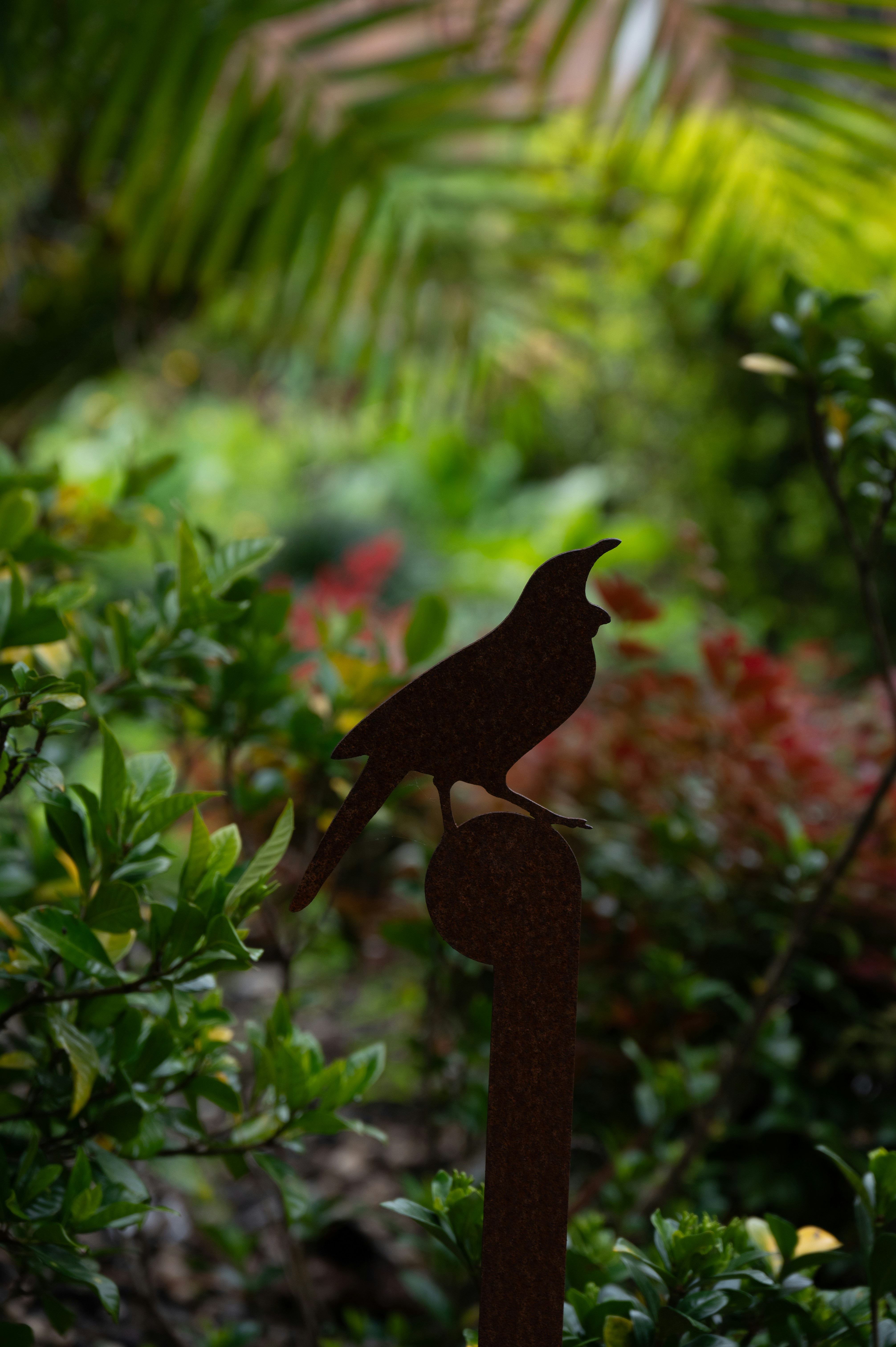 Rusted crow silhouette perches on a garden stake amid tropical foliage