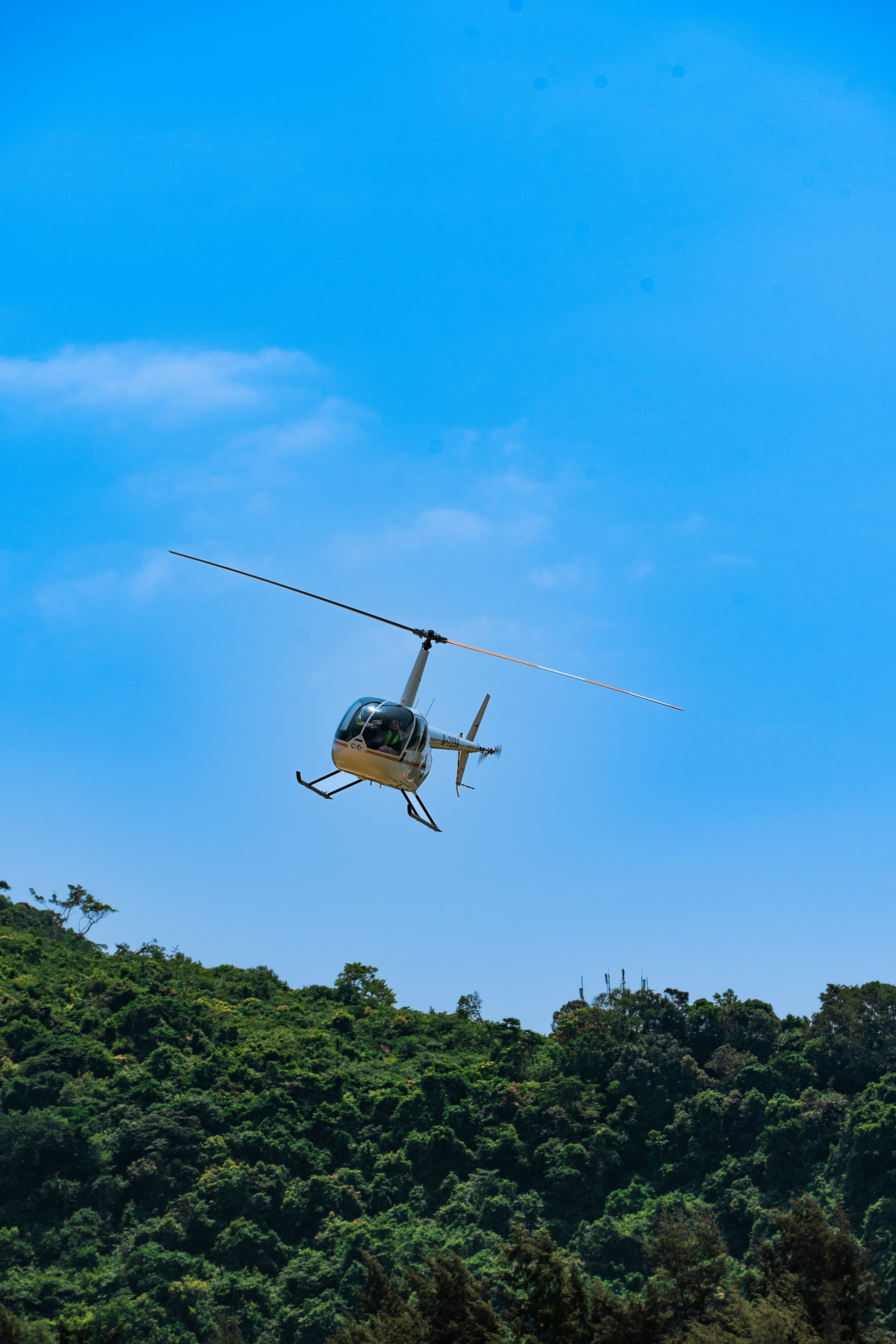 Blue Sky Hover: A solitary helicopter over emerald ridges