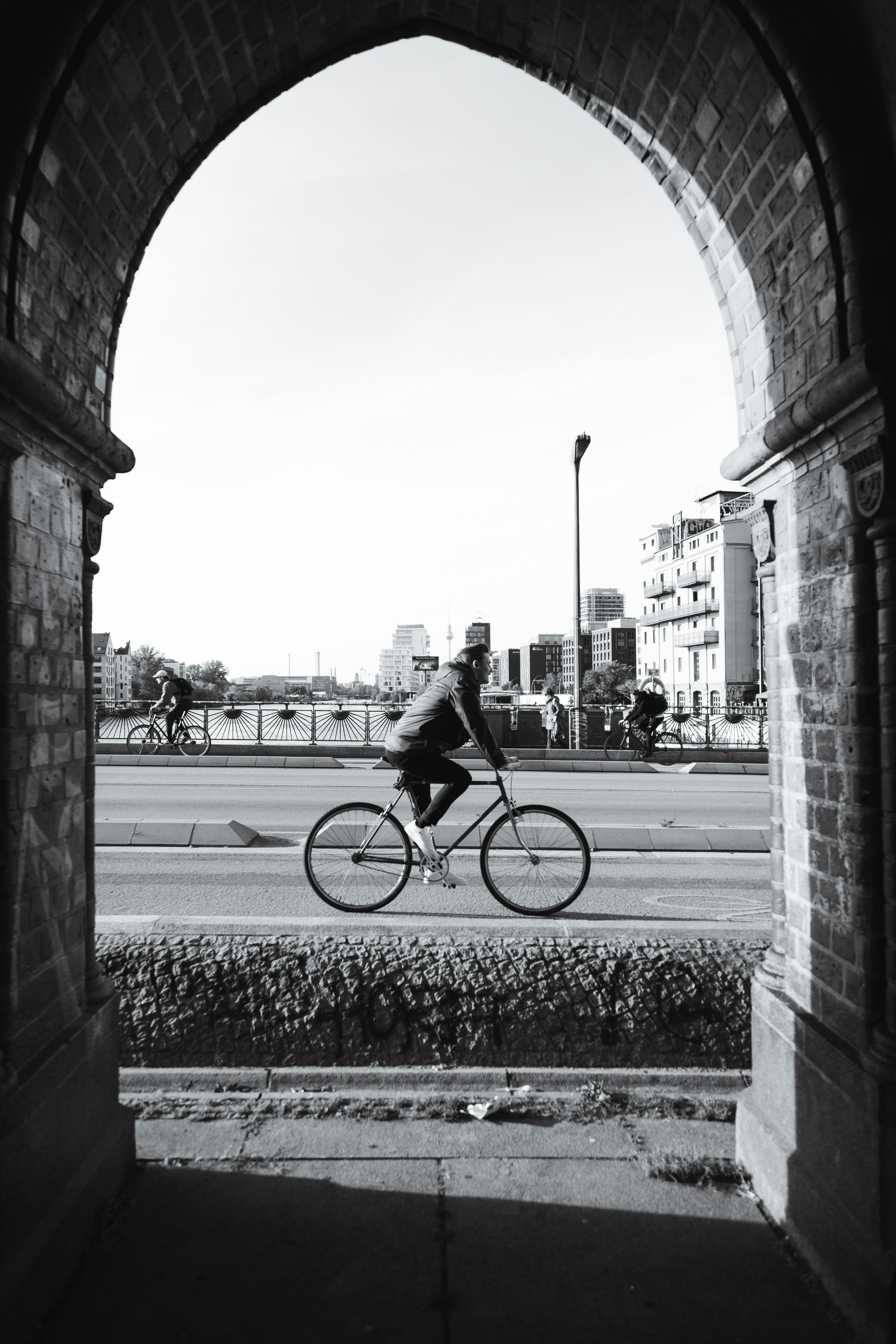 Archway Crossing: A Cyclist Threads the Monochrome Riverfront Frame