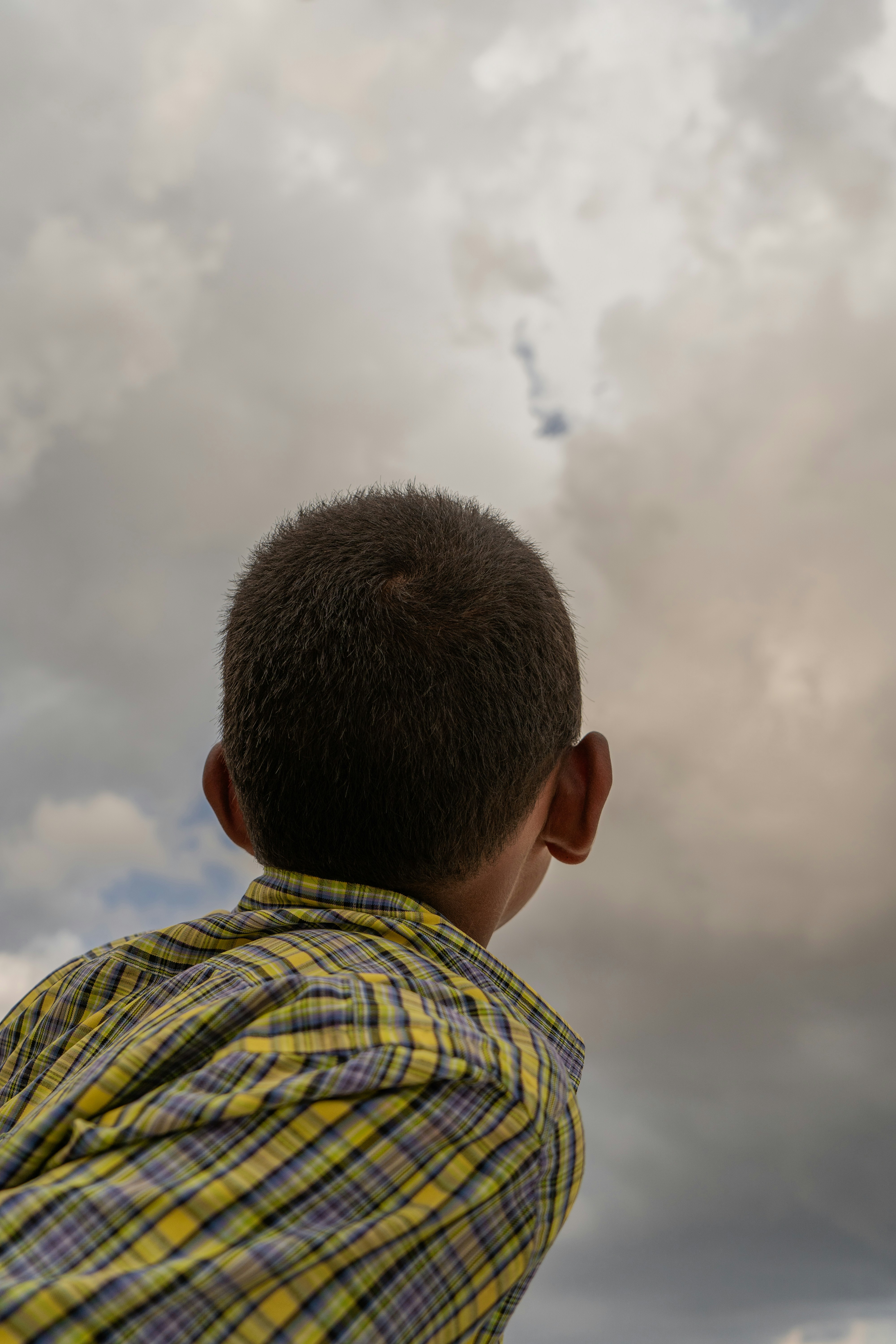 Gaze Upward in Plaid: A Boy Against a Cloudy Sky