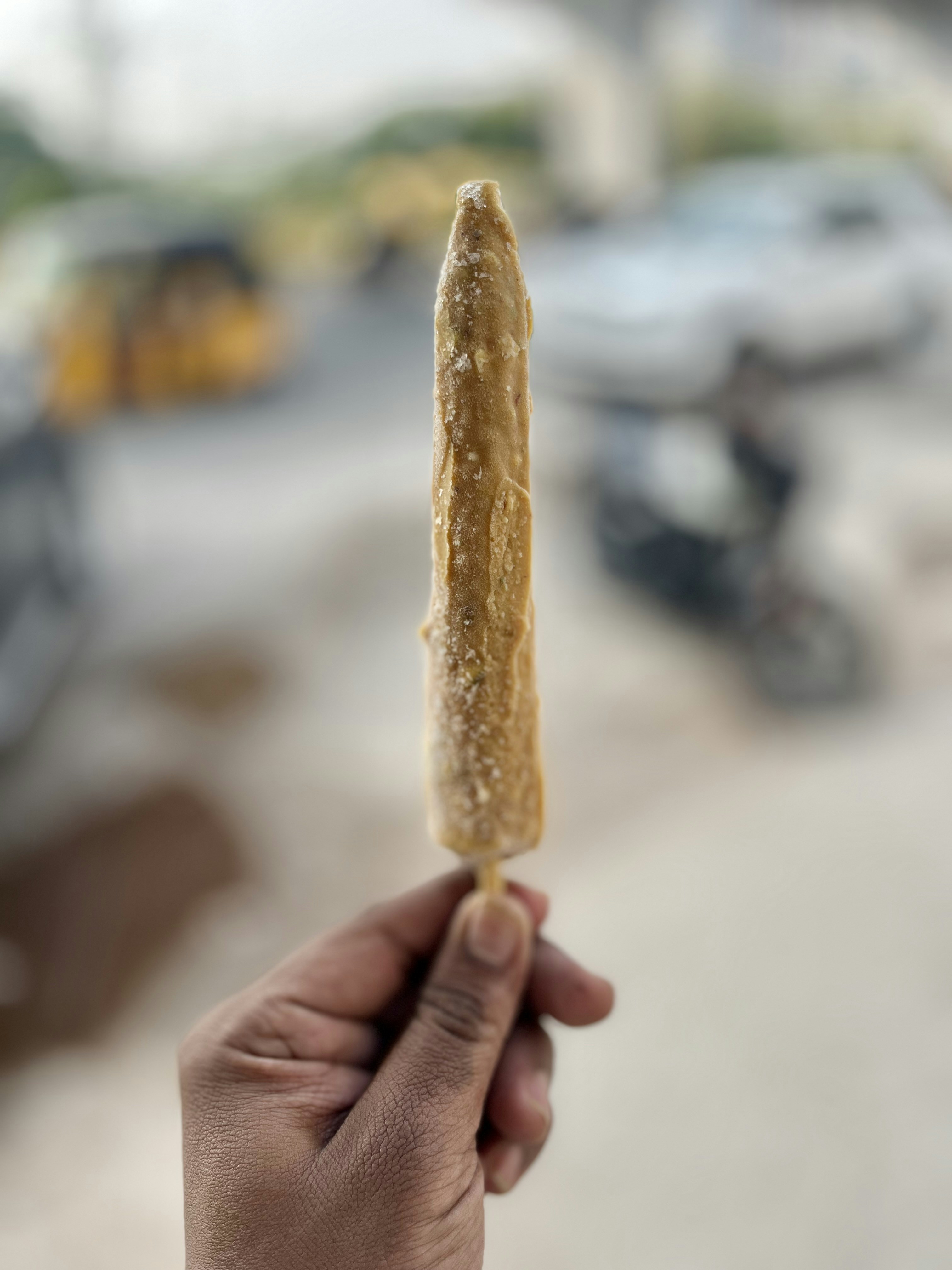 Center Stage Snack: A Golden Corn Dog in Focus Amid a Gentle City Blur