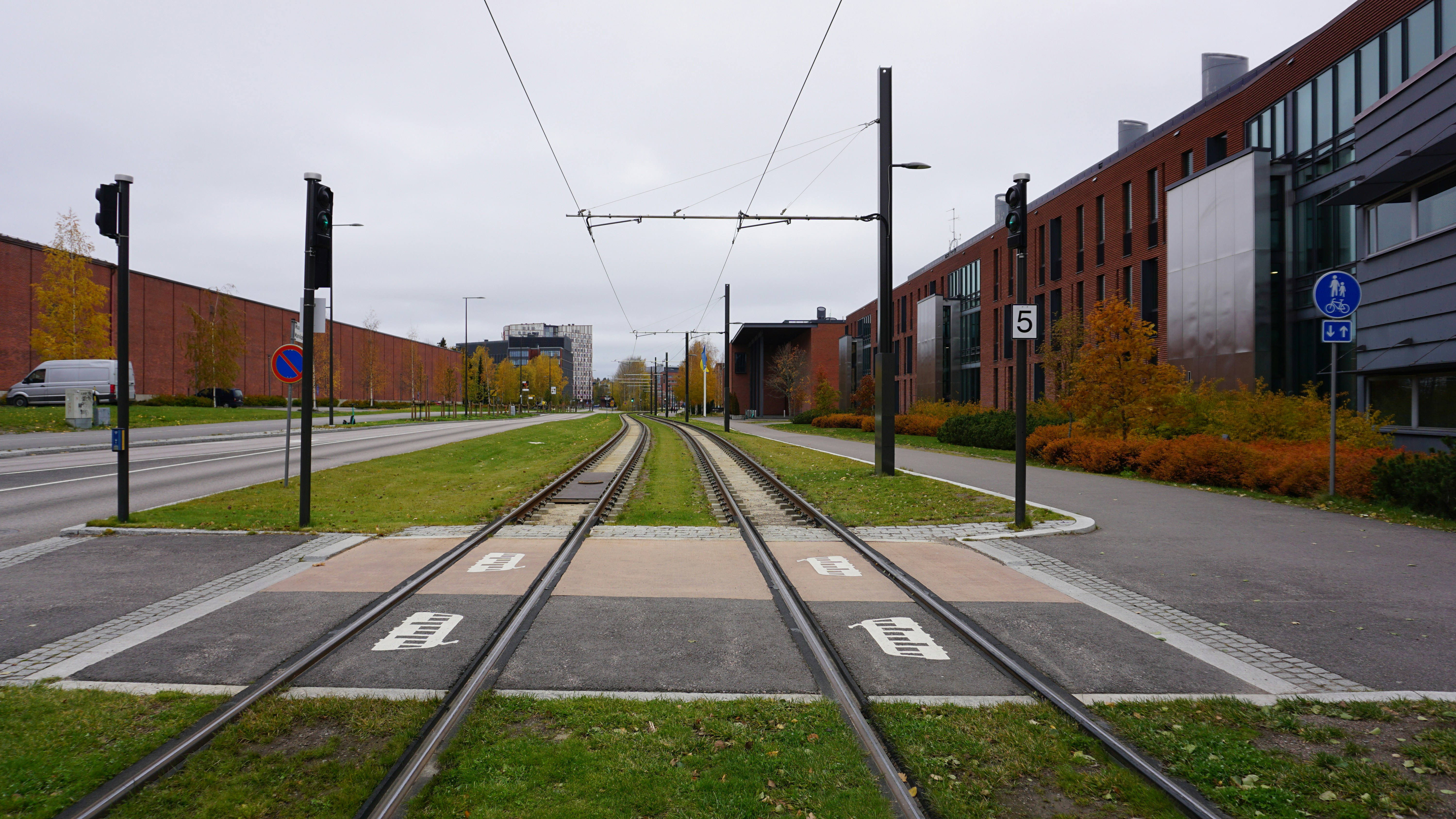 Symmetrical tram tracks leading through an urban landscape with modern architecture and autumn foliage.