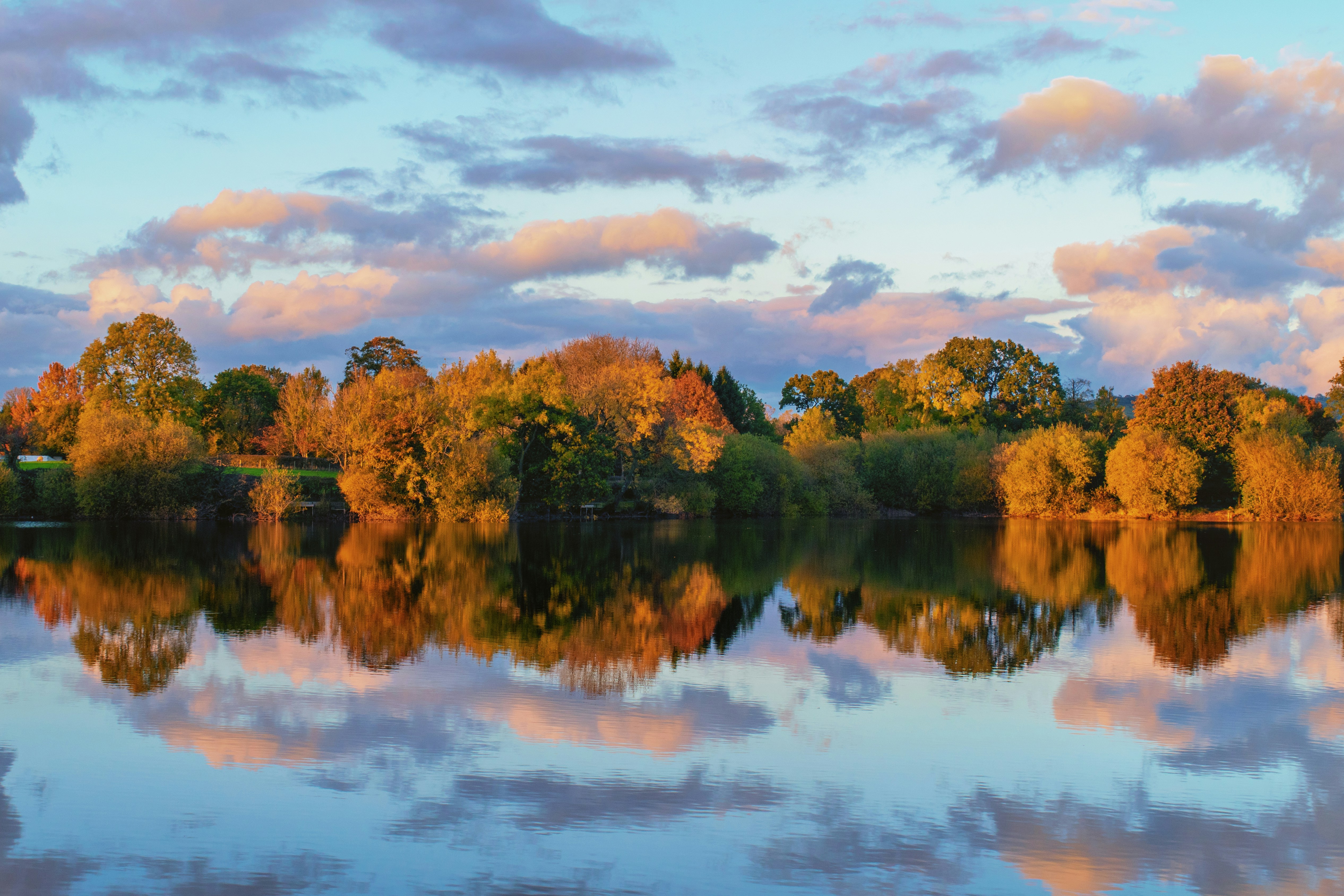 Autumn trees and clouds perfectly mirrored on a serene lake under a vibrant sky.