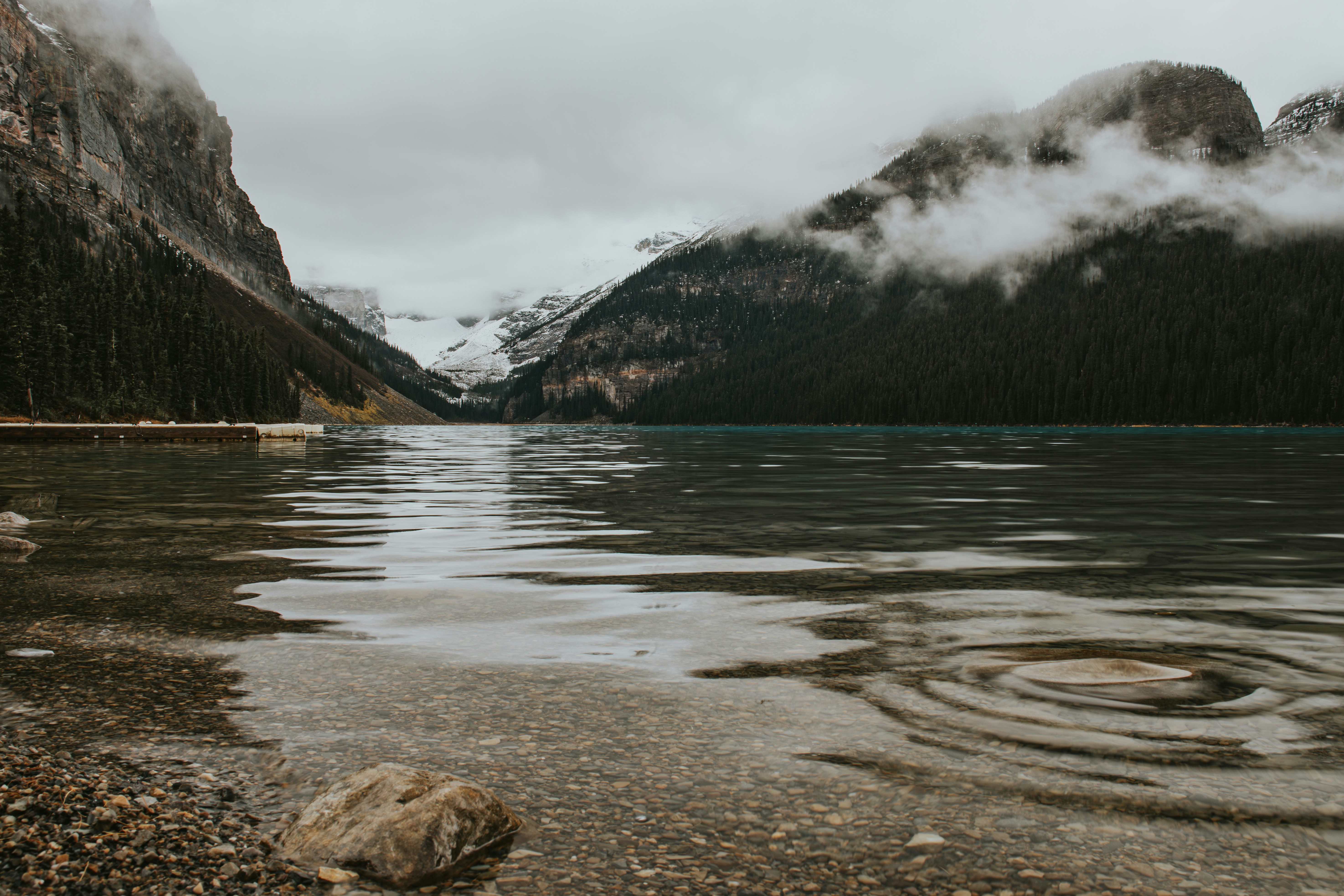 Mountain lake with gentle ripples and mist-covered peaks under an overcast sky.