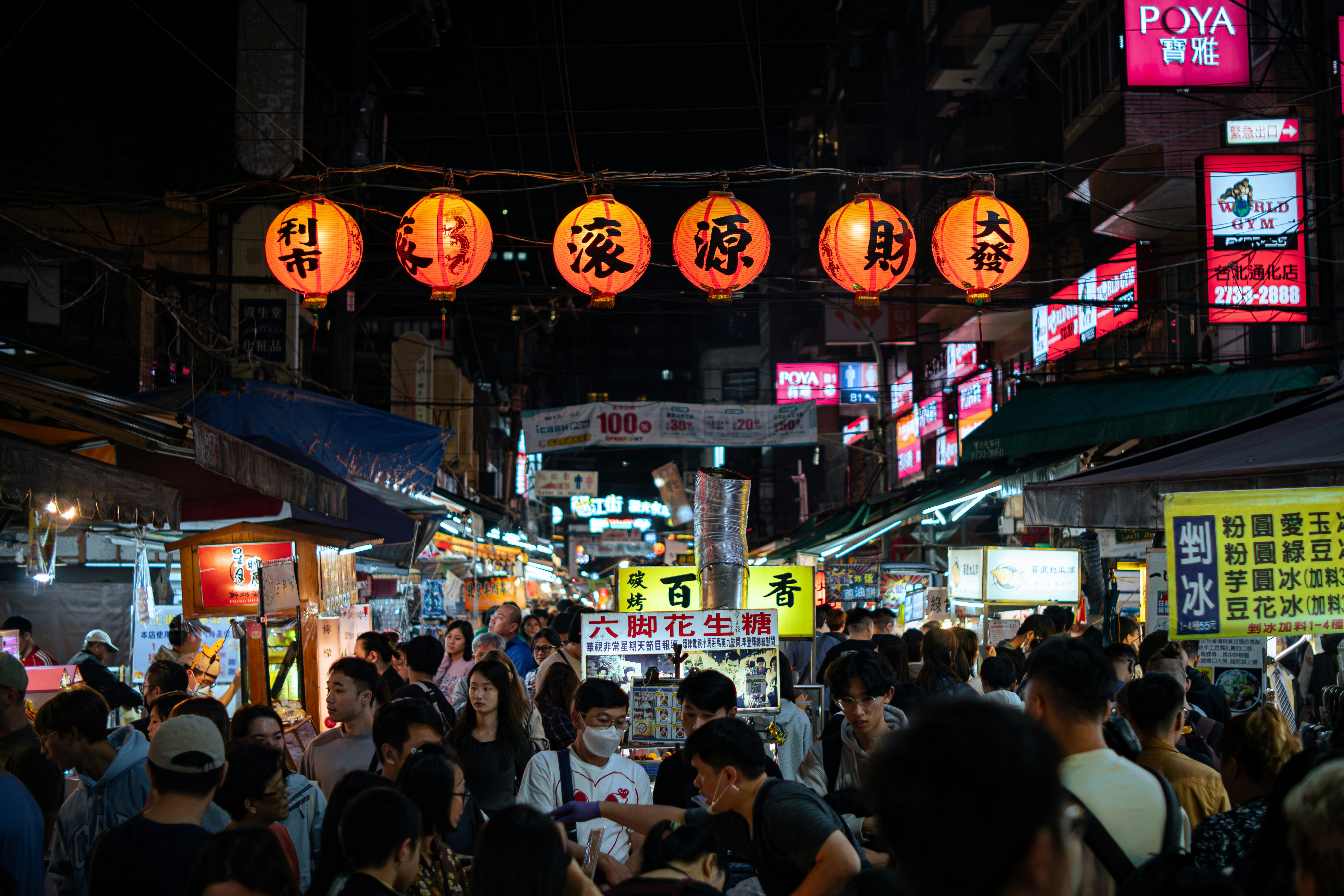 Crowded street market illuminated by glowing lanterns and neon signs at night.