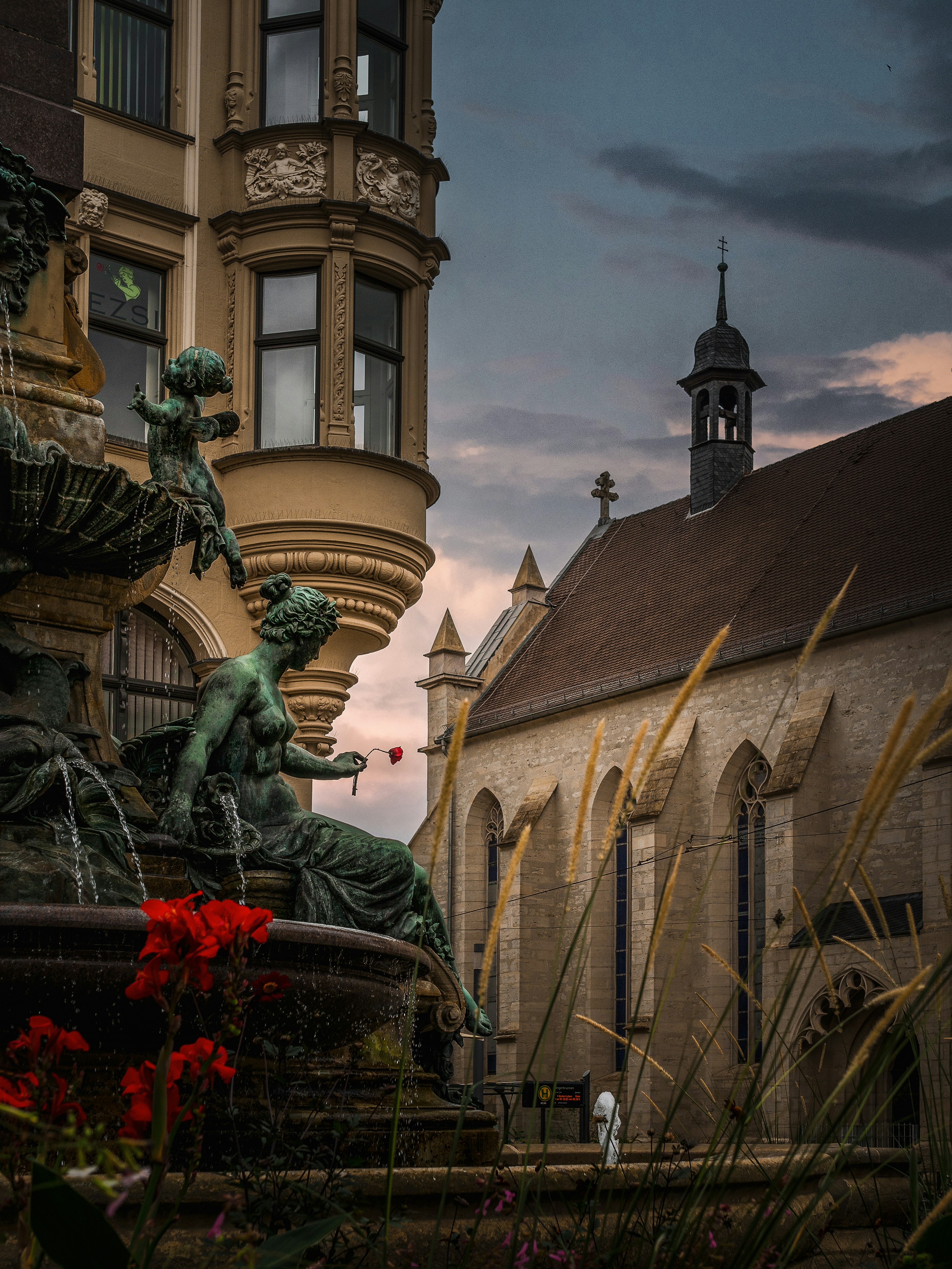 Twilight at the Town Fountain: Bronze Statues and Gothic Spires in Soft Light