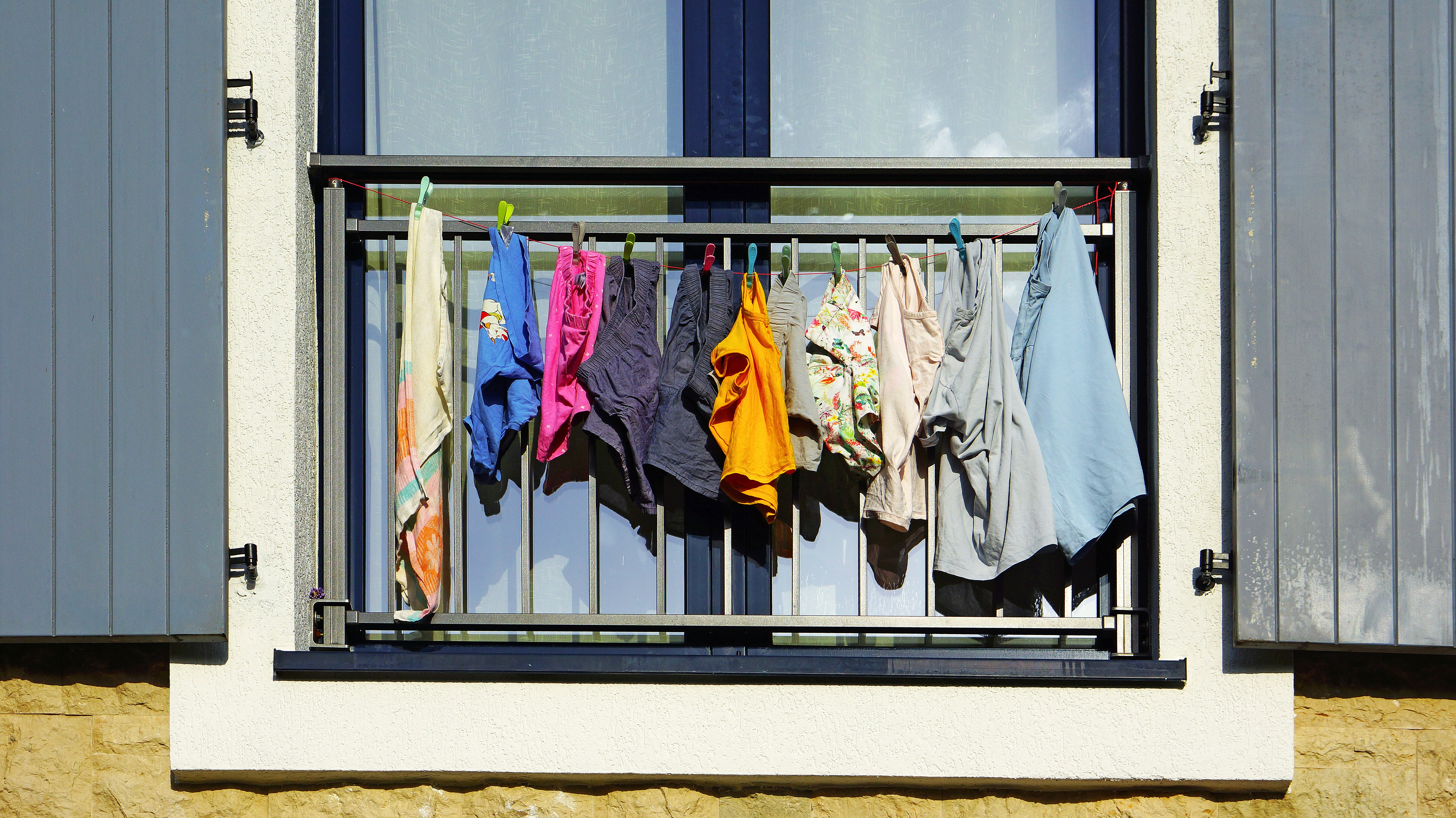 Sunlit Balcony Laundry: Colorful Fabrics Draped Under Blue Shutters