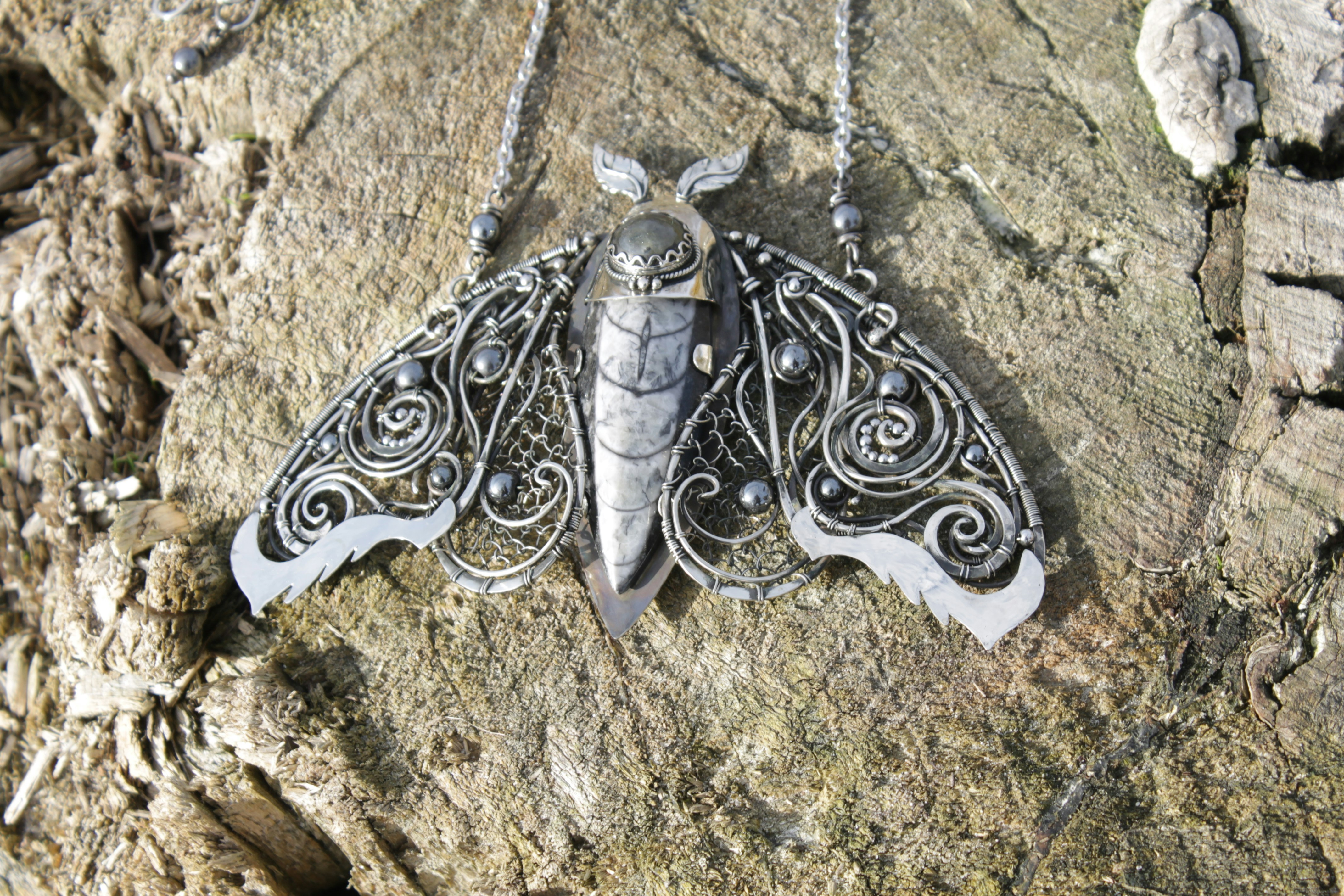 Ornate moth pendant resting on weathered stone