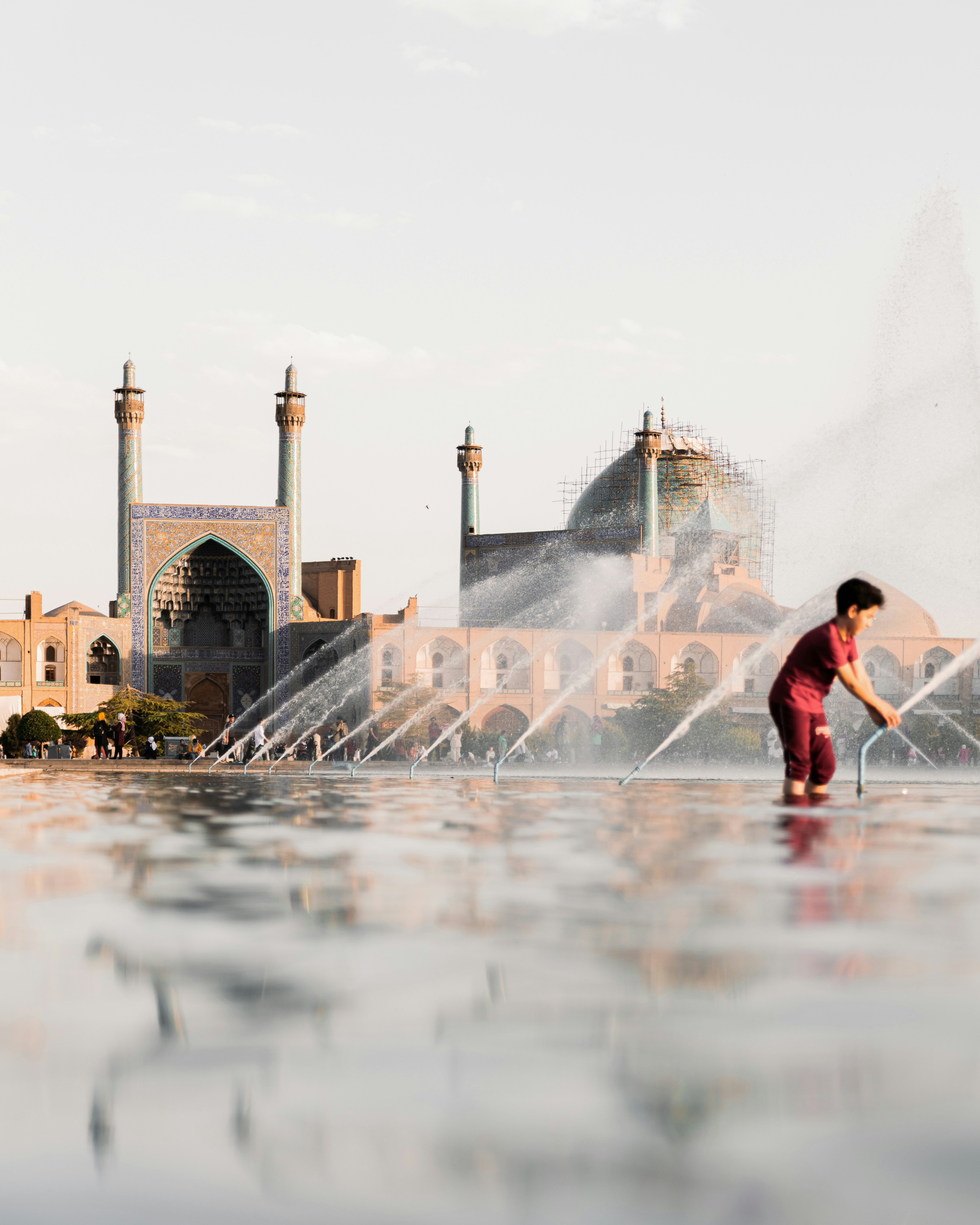 Red-Clad Child Amid Fountains in a Tile-Arcade Courtyard