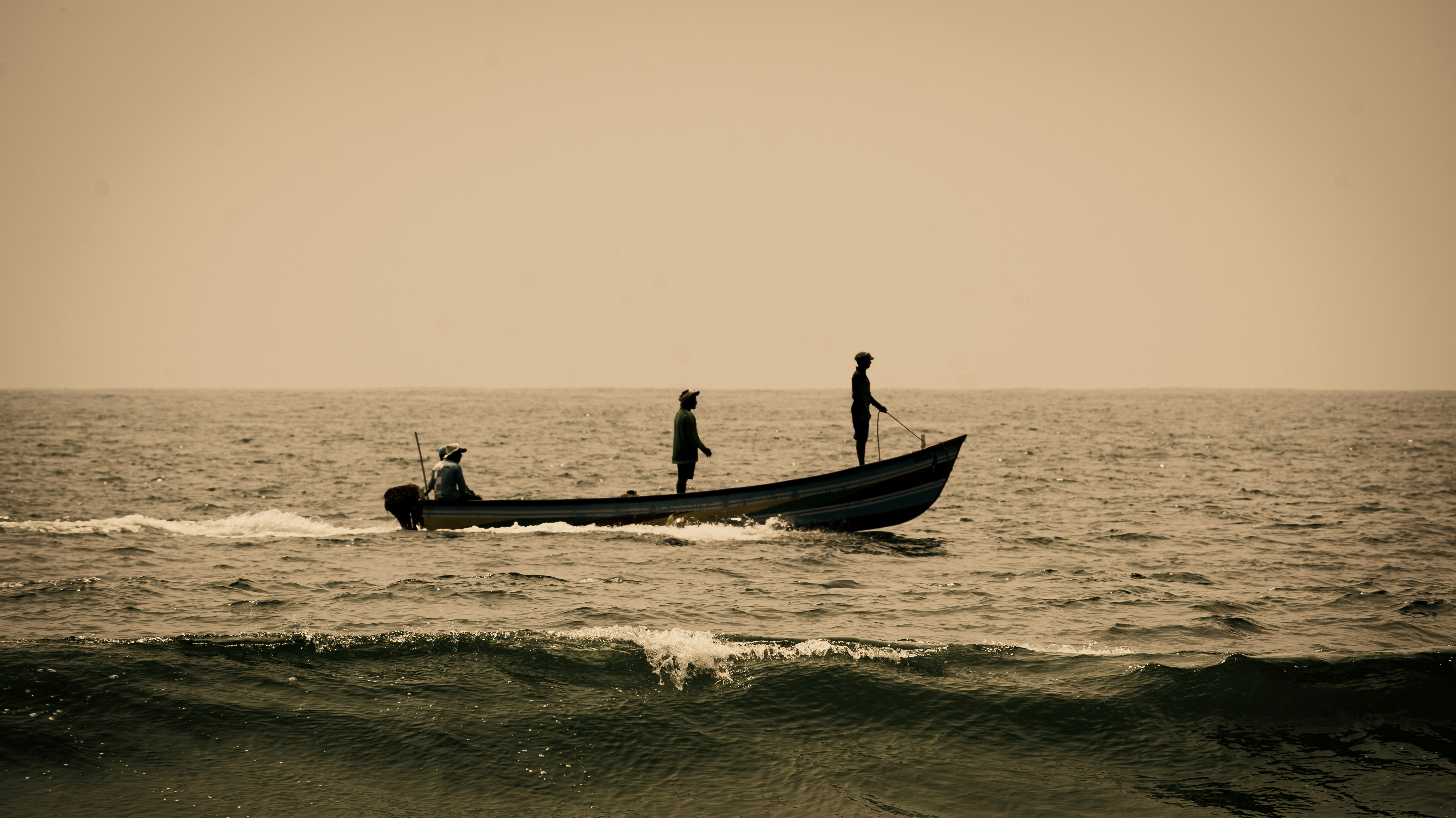 Three figures navigate a small boat across gentle ocean waves under a sepia-toned sky.