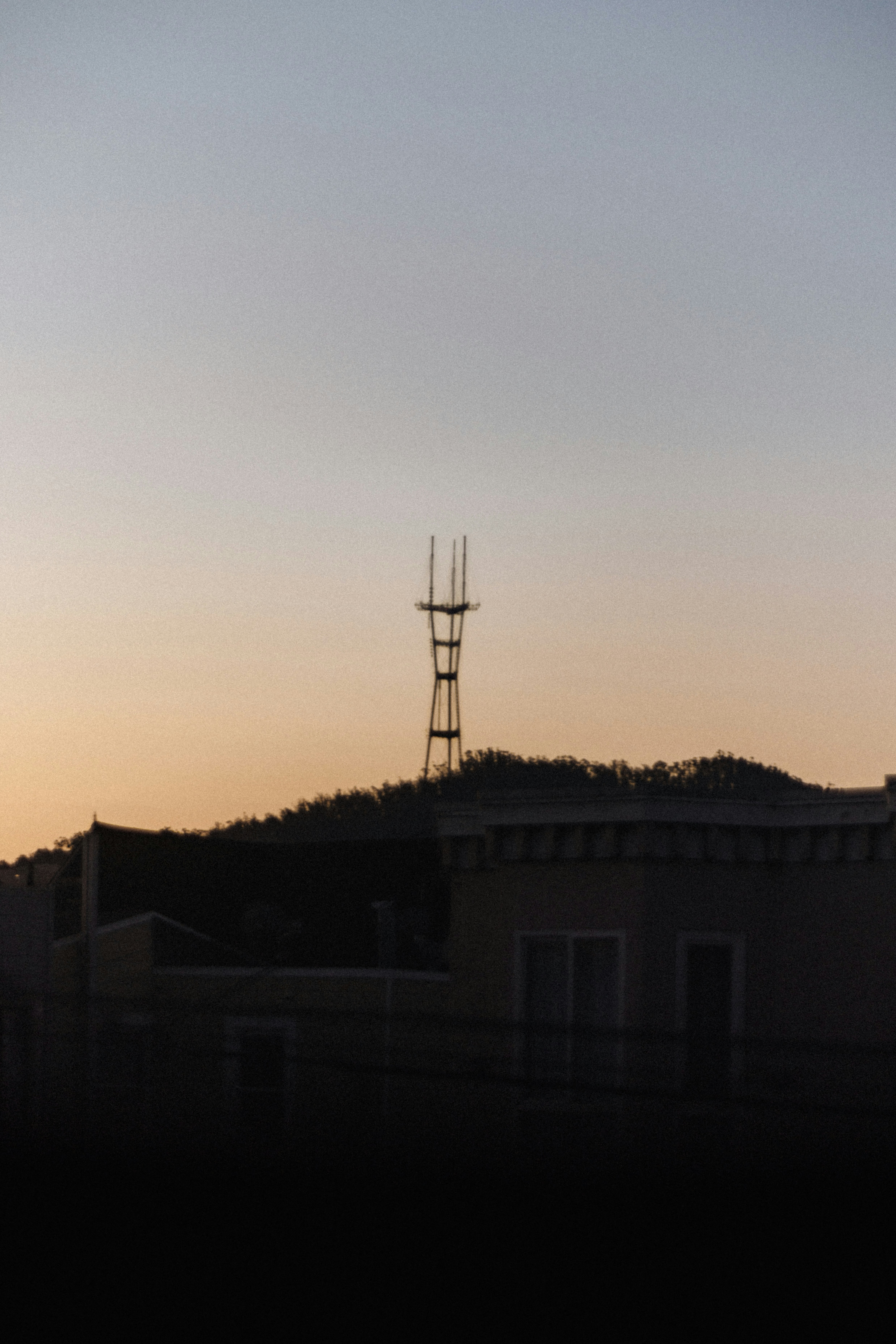 Dusk Crown: A solitary transmission tower silhouetted against a quiet rooftop skyline.