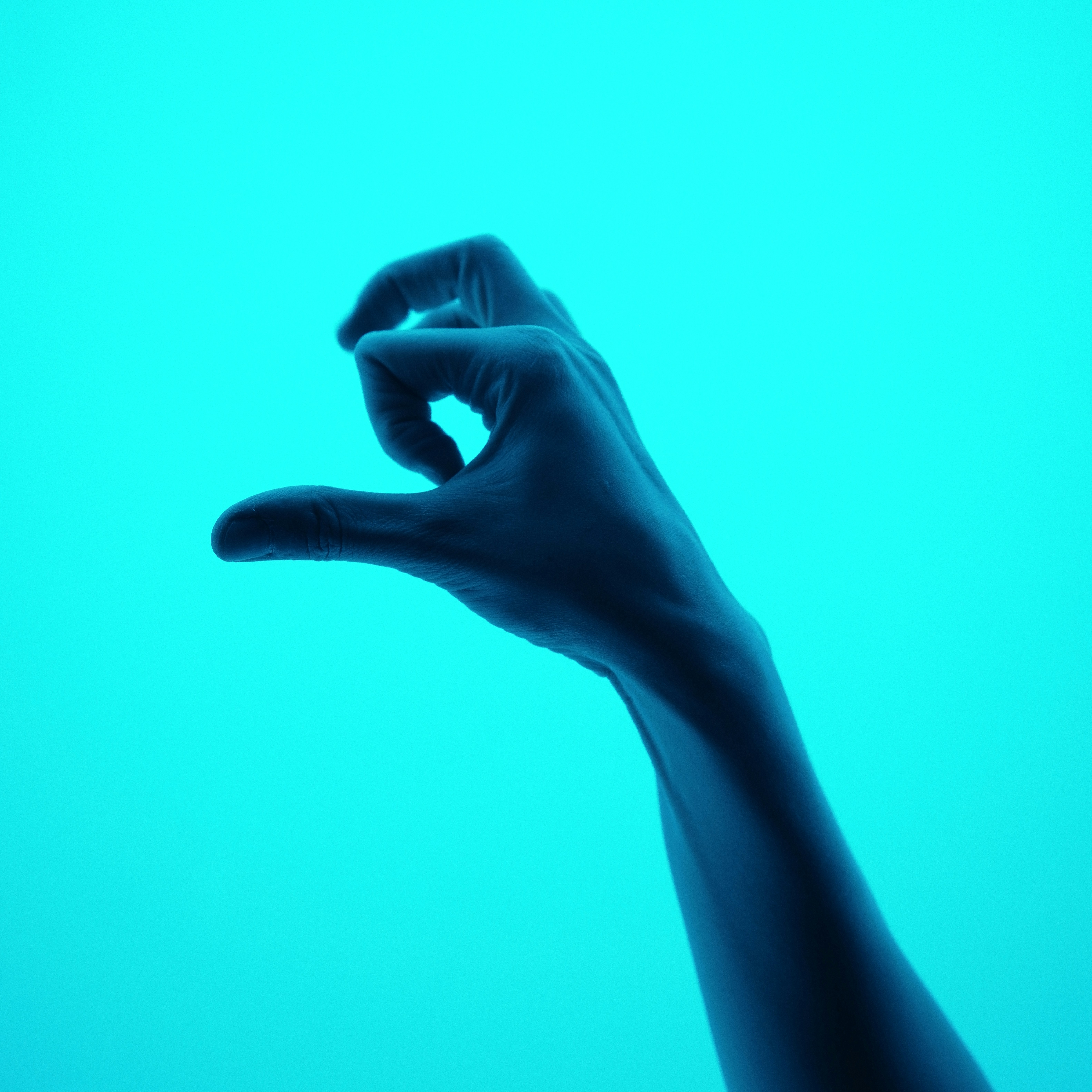 Amid a cyan backdrop, a hand forms a tiny pinch between thumb and forefinger. This photograph emphasizes shape and negative space.