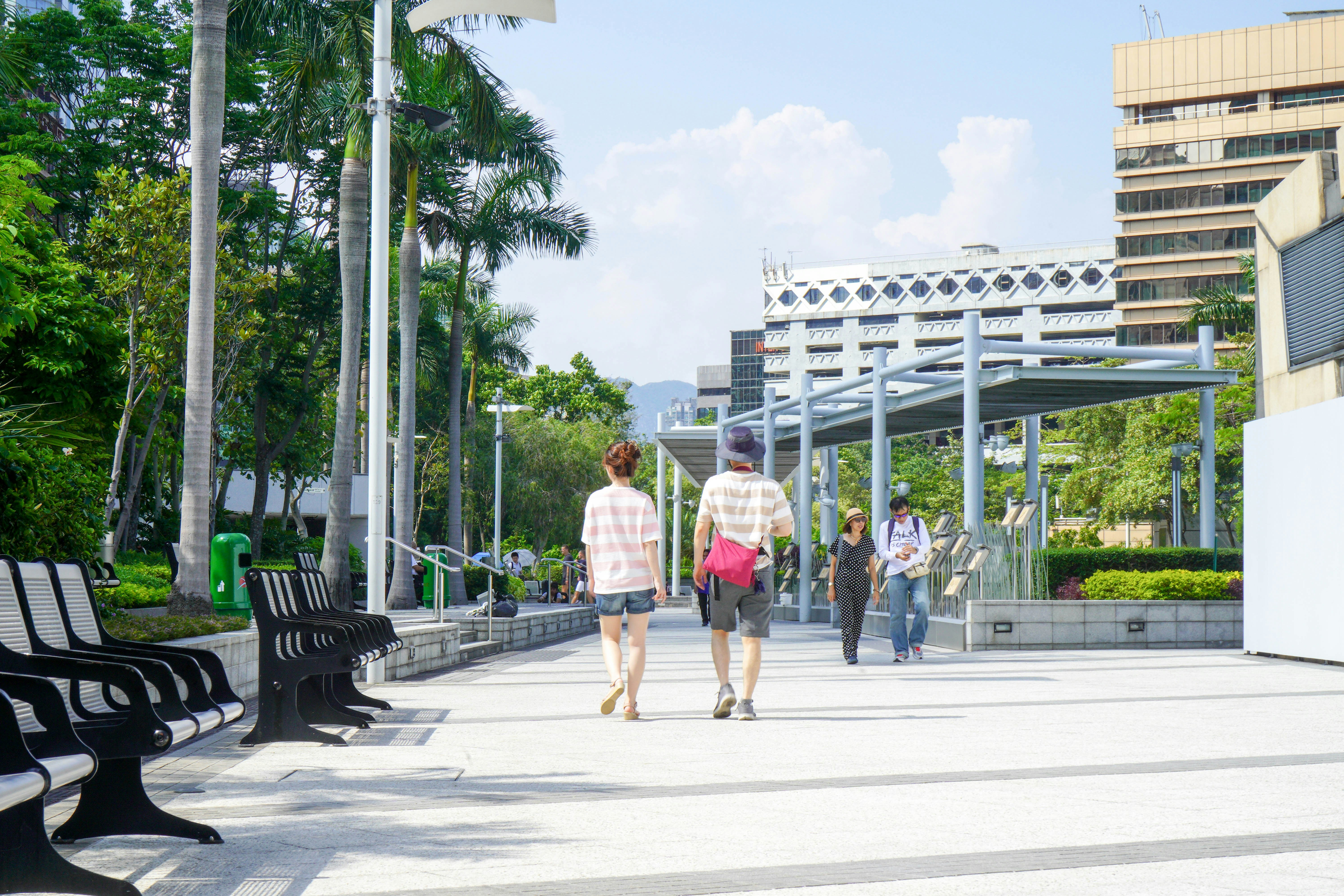 A group of people walking down a sidewalk next to benches photo – Free ...