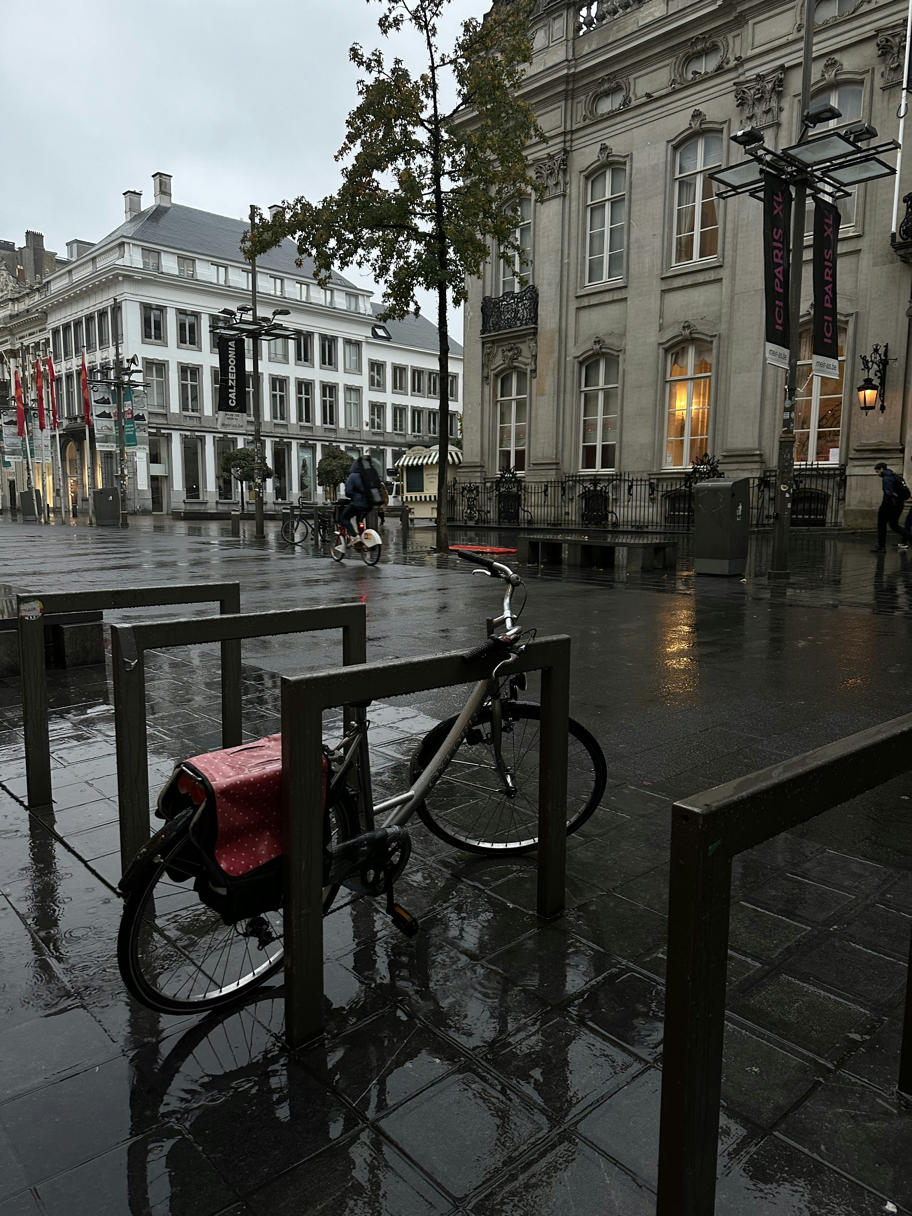 Rain-Soaked City Square: A Red-Pannier Bicycle Anchored at the Rails