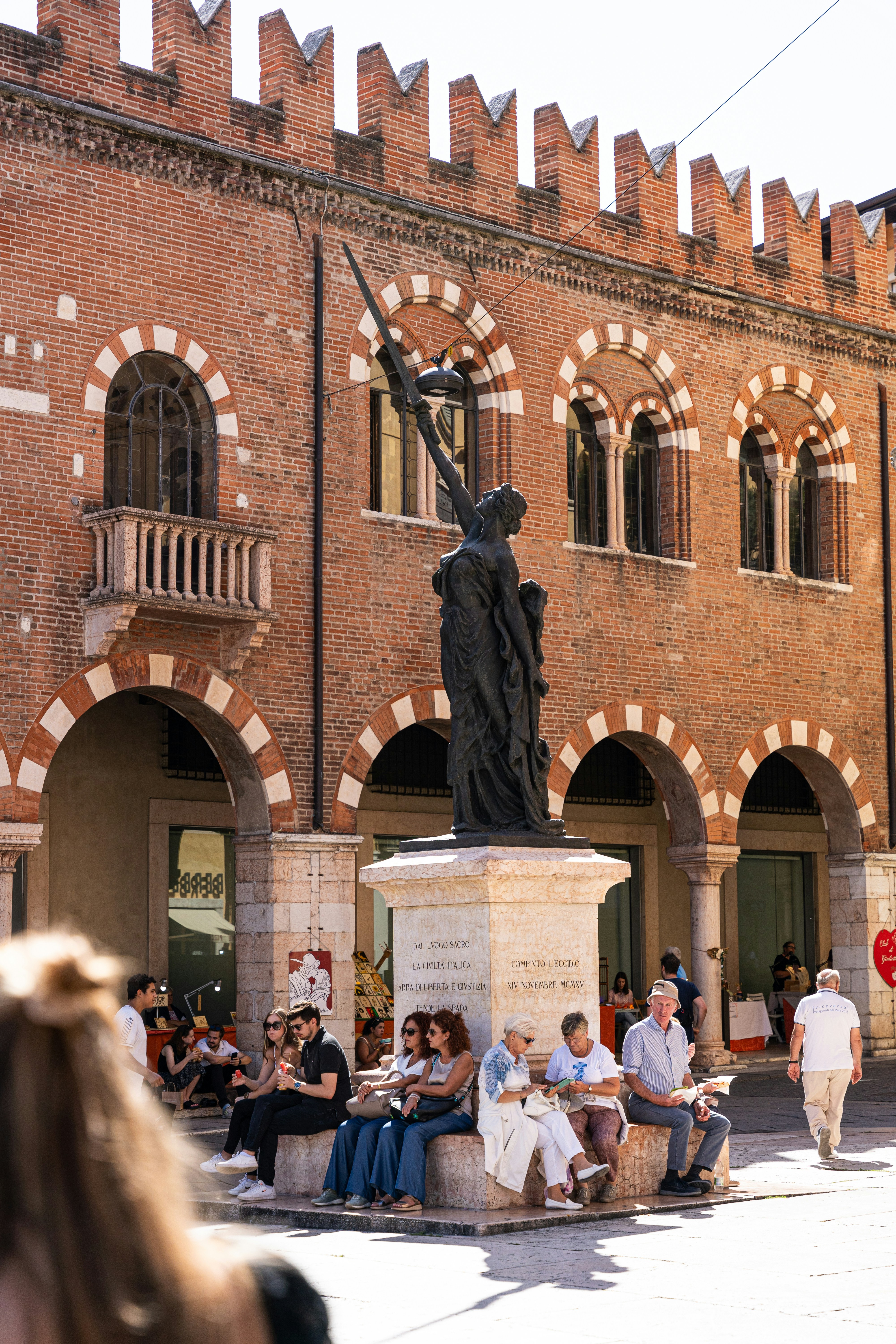 Statue in the sunlit plaza framed by brick arches