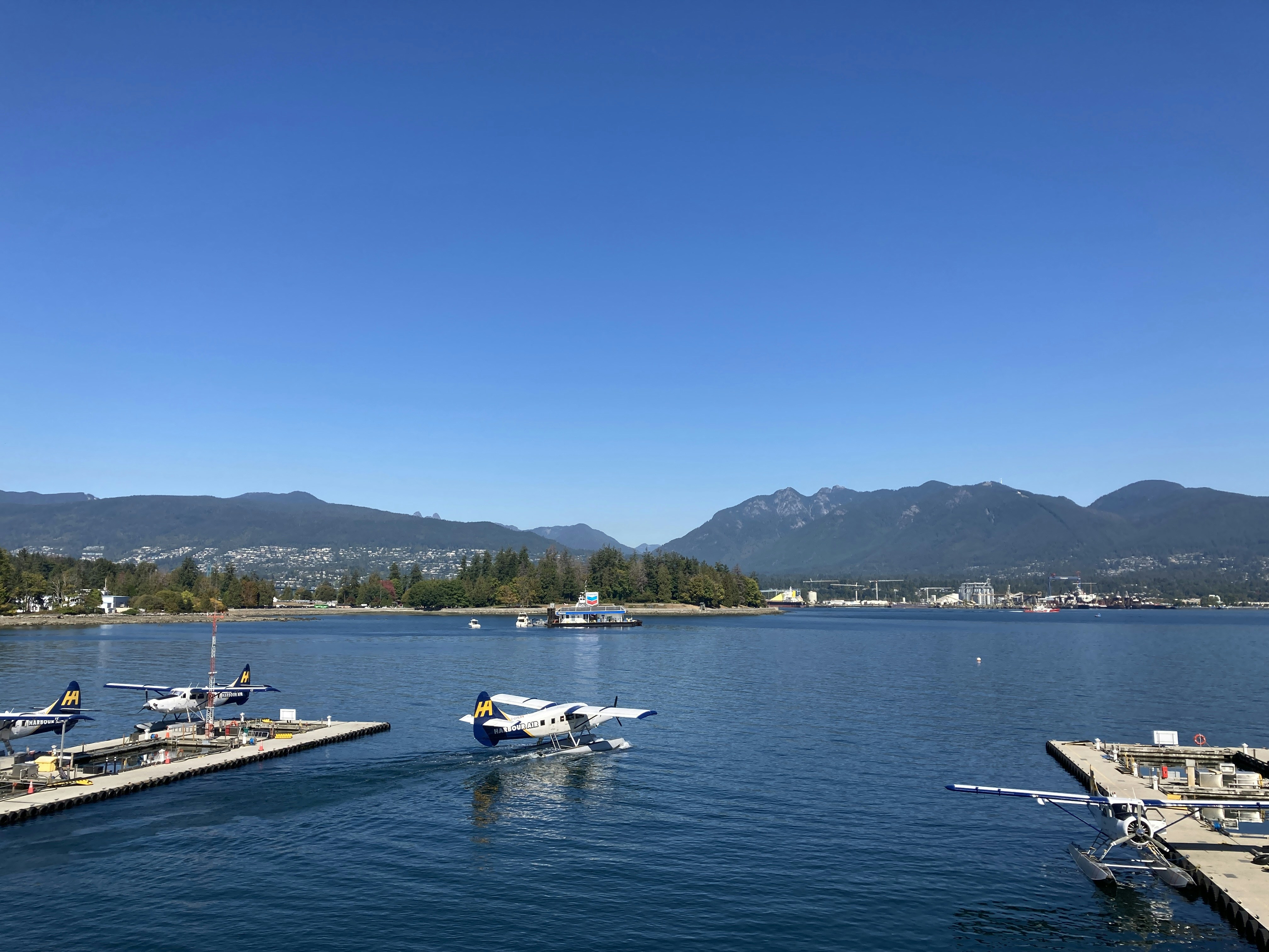 Seaplanes docked at a harbor with mountains in the background under a clear blue sky. The calm water reflects the serene landscape.