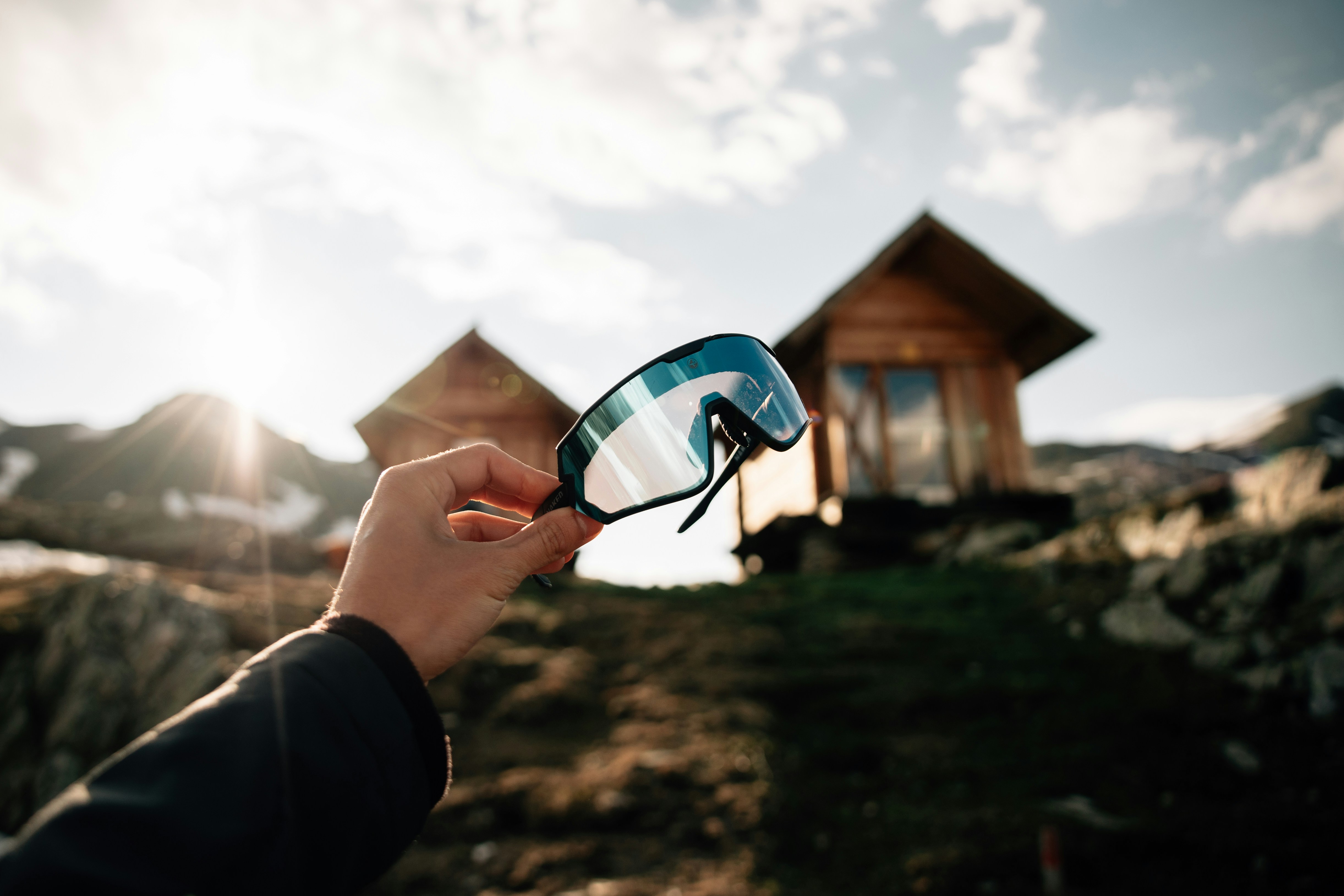 Foreground Sunglasses Frame a Rustic Sunrise Over Alpine Cabins