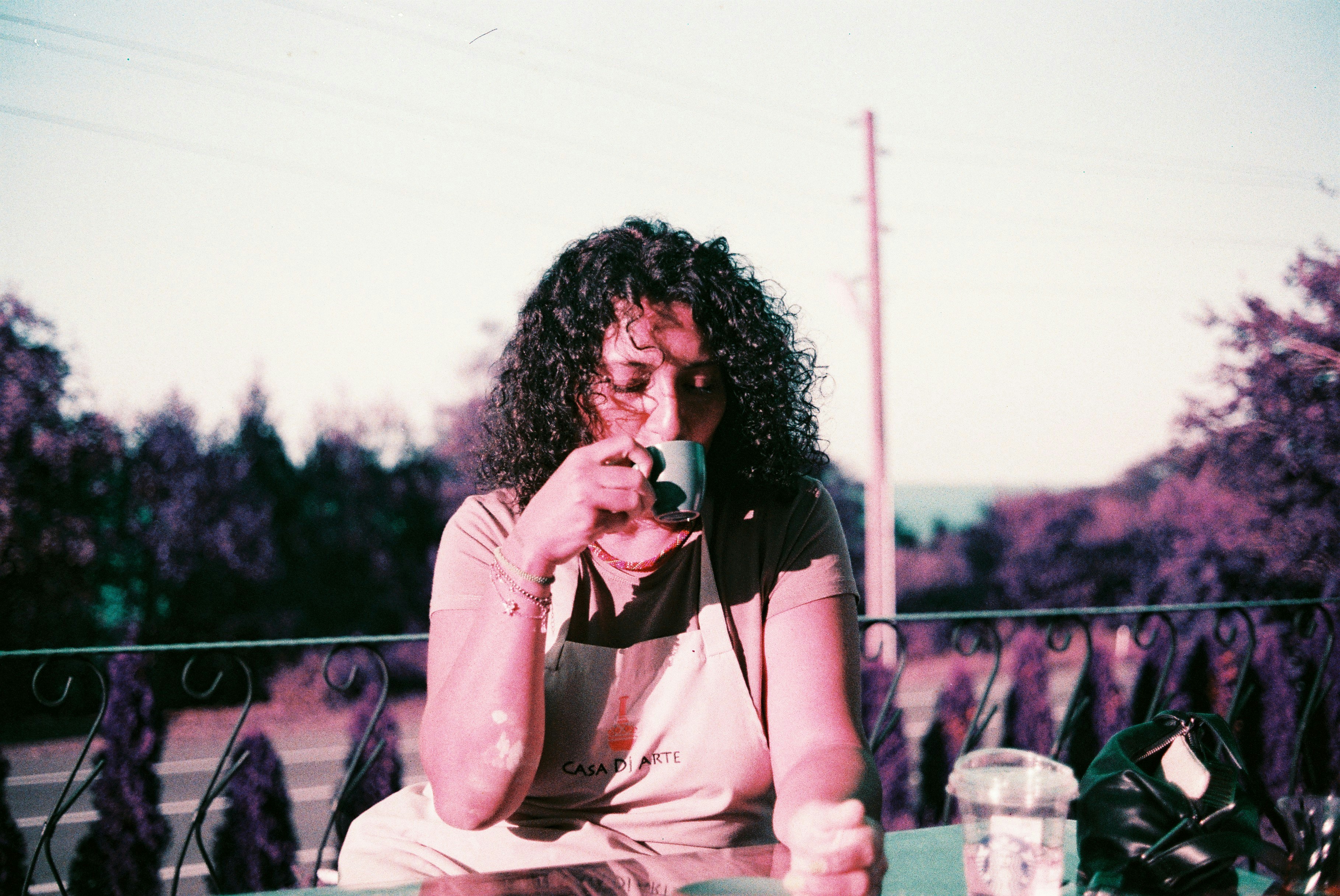 Person sipping coffee on a terrace with a surreal purple-tinted landscape.