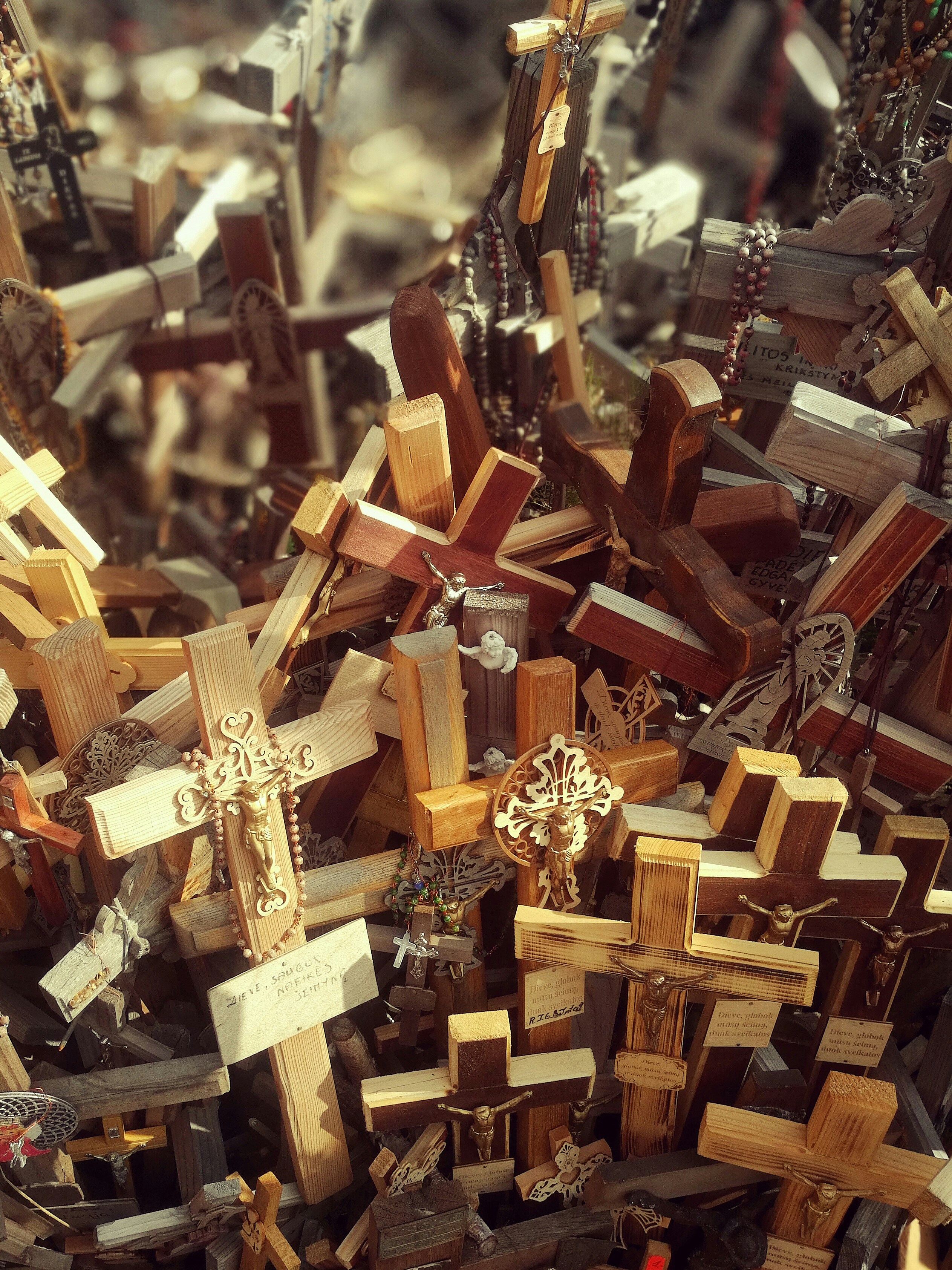 A dense clutter of wooden crucifixes and rosaries forms a devotional still-life, stacking light and shadow in a crowded display.