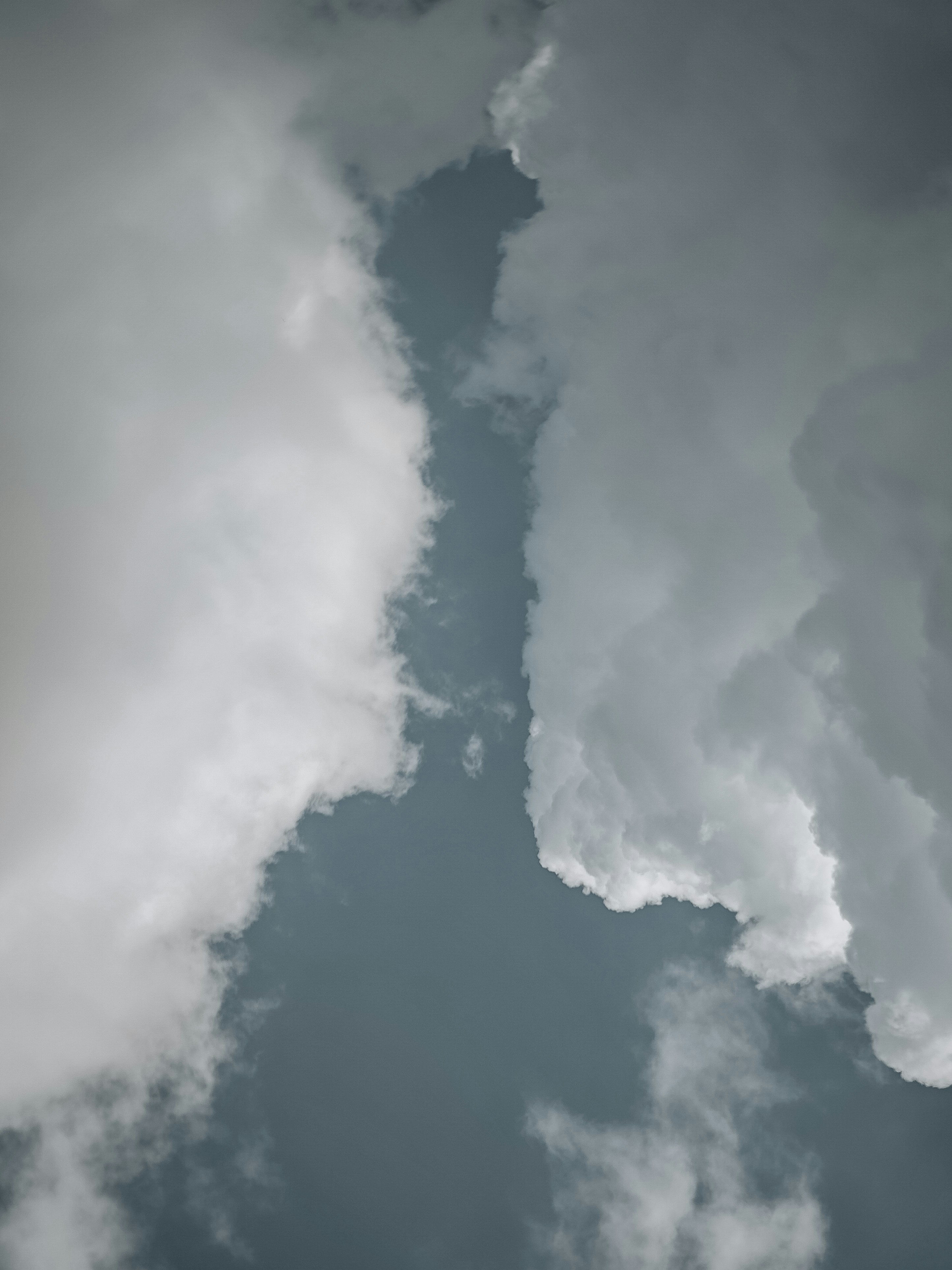 Clouds form a slender vertical gap revealing blue sky, creating stark negative space in this photograph.