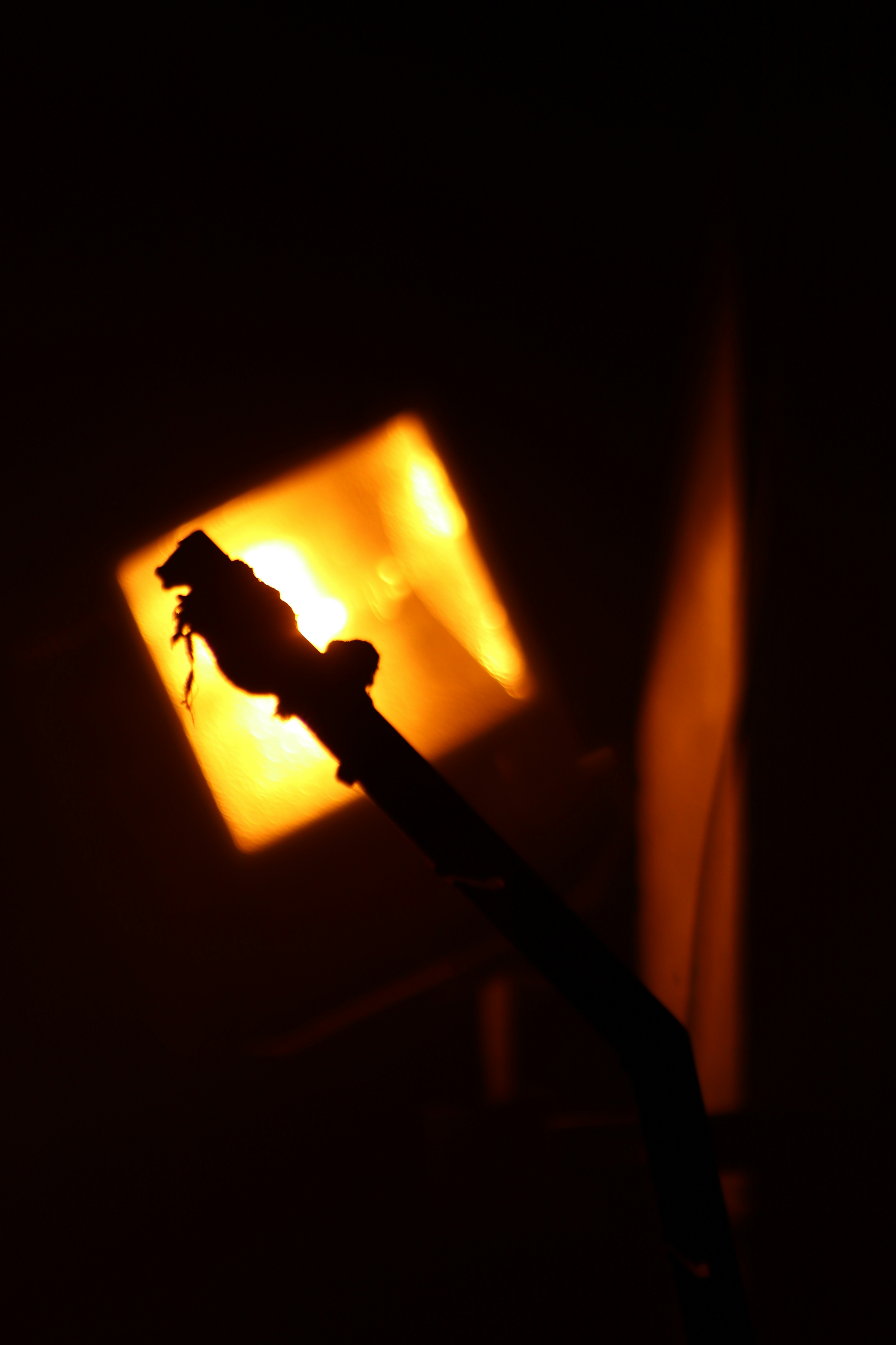 Silhouette of a lamp arm against a glowing light source, creating a dramatic contrast. The warm light casts intriguing shapes in the surrounding darkness.