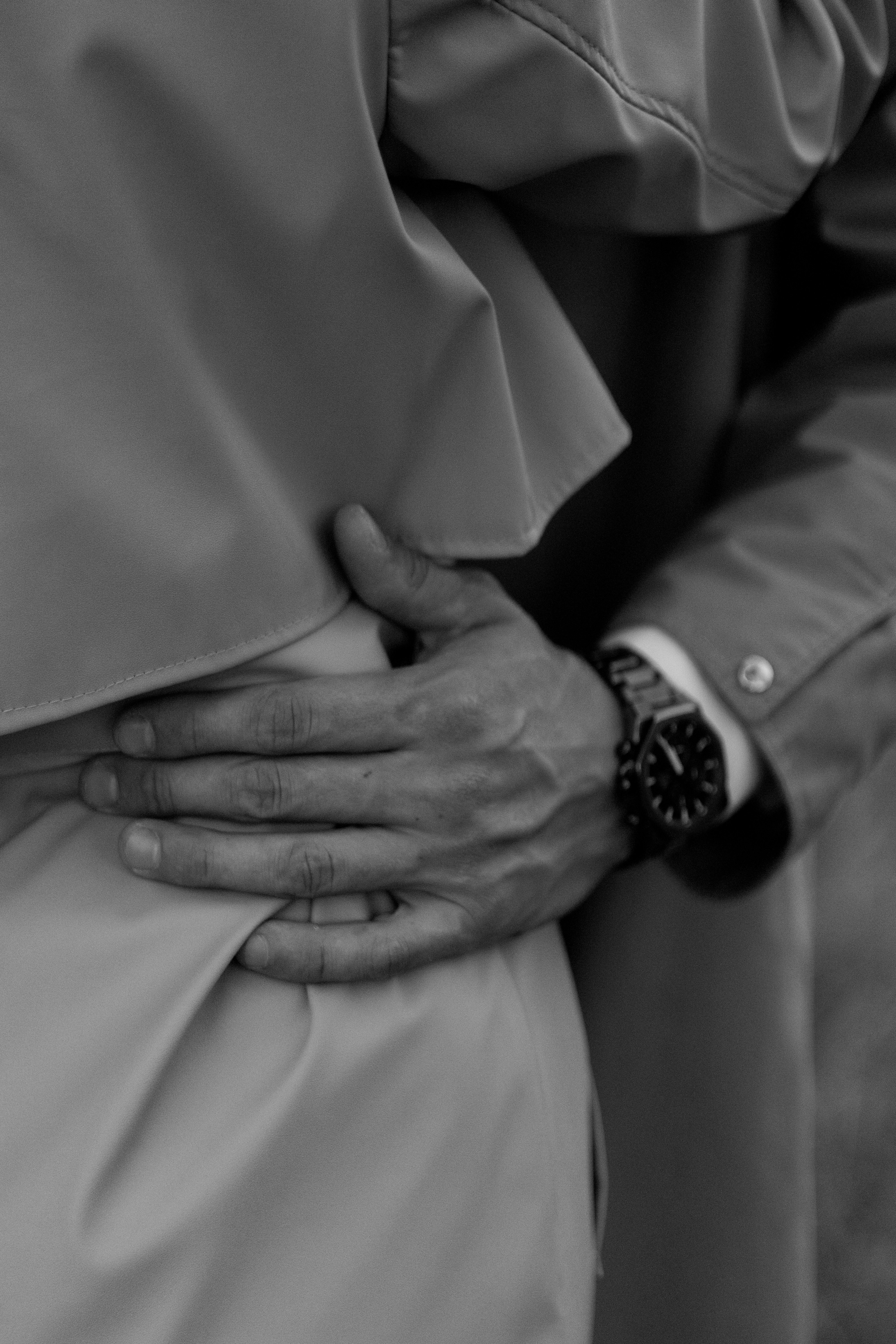 Close-up of a couple in an intimate embrace, highlighting the hands and clothing details in black and white.