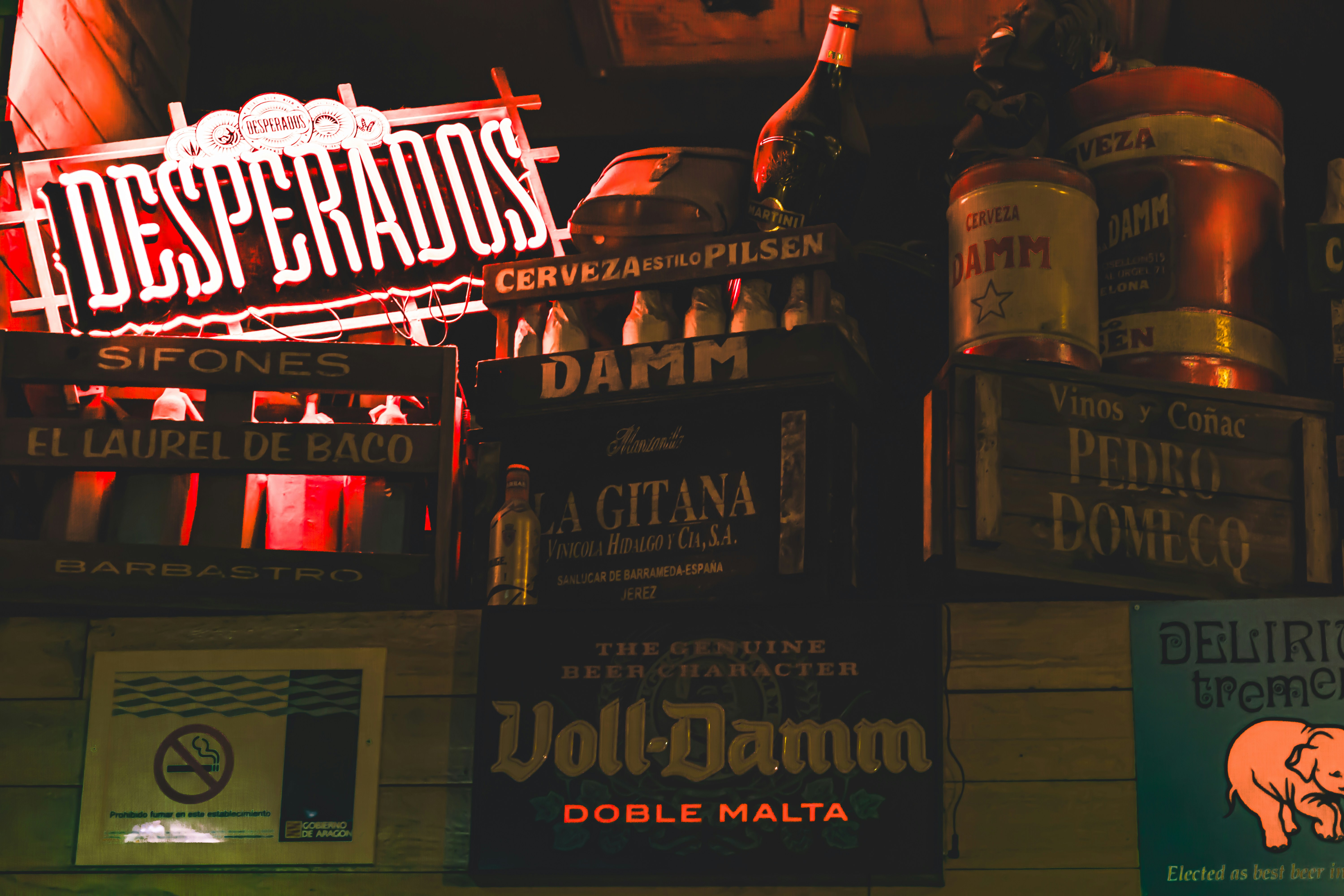 A neon sign that reads desperados above a display of liquor bottles ...