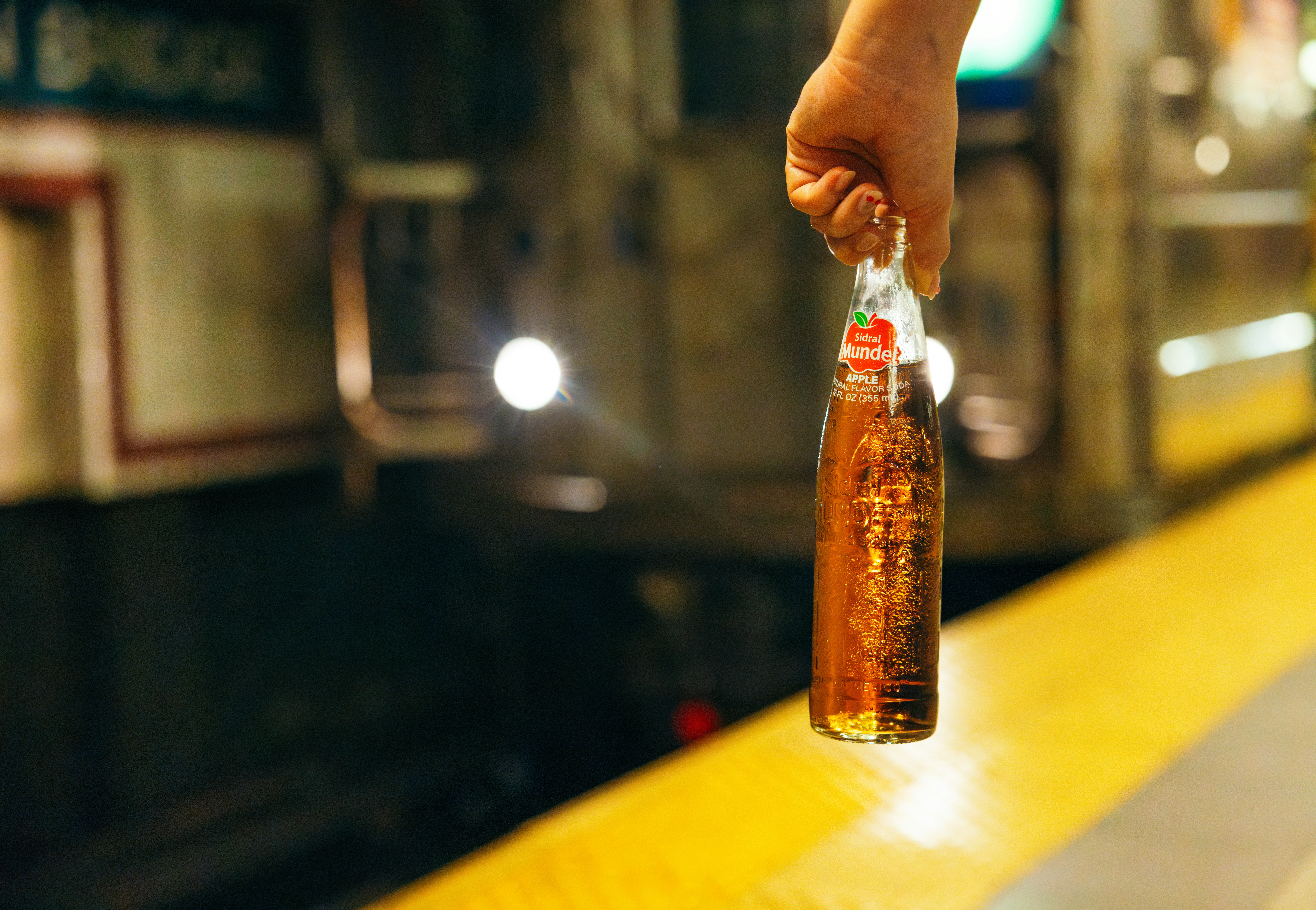 A person holding a bottle of beer on a train platform photo – Free Soda ...