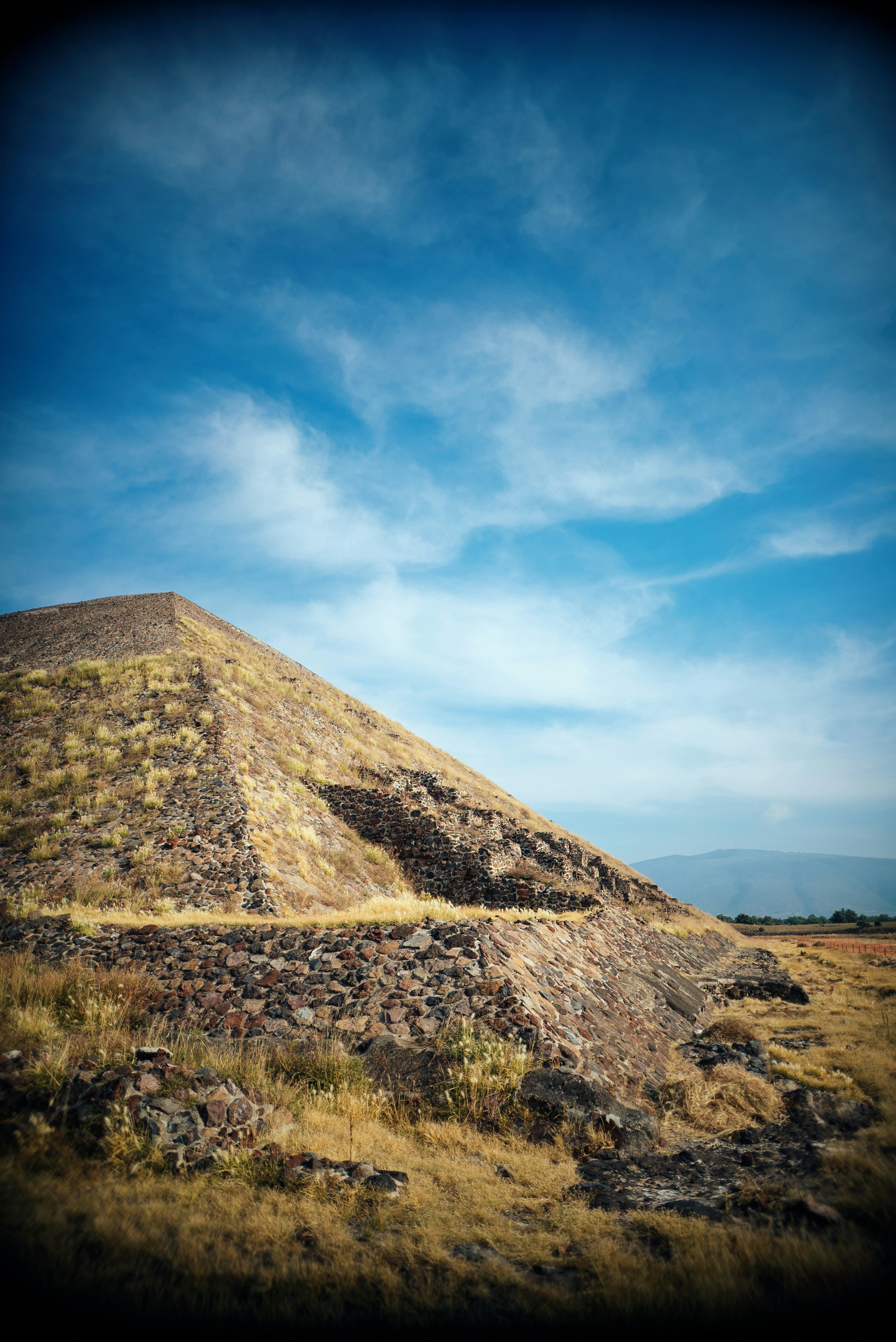 Ancient pyramid under a vibrant blue sky with scattered clouds.